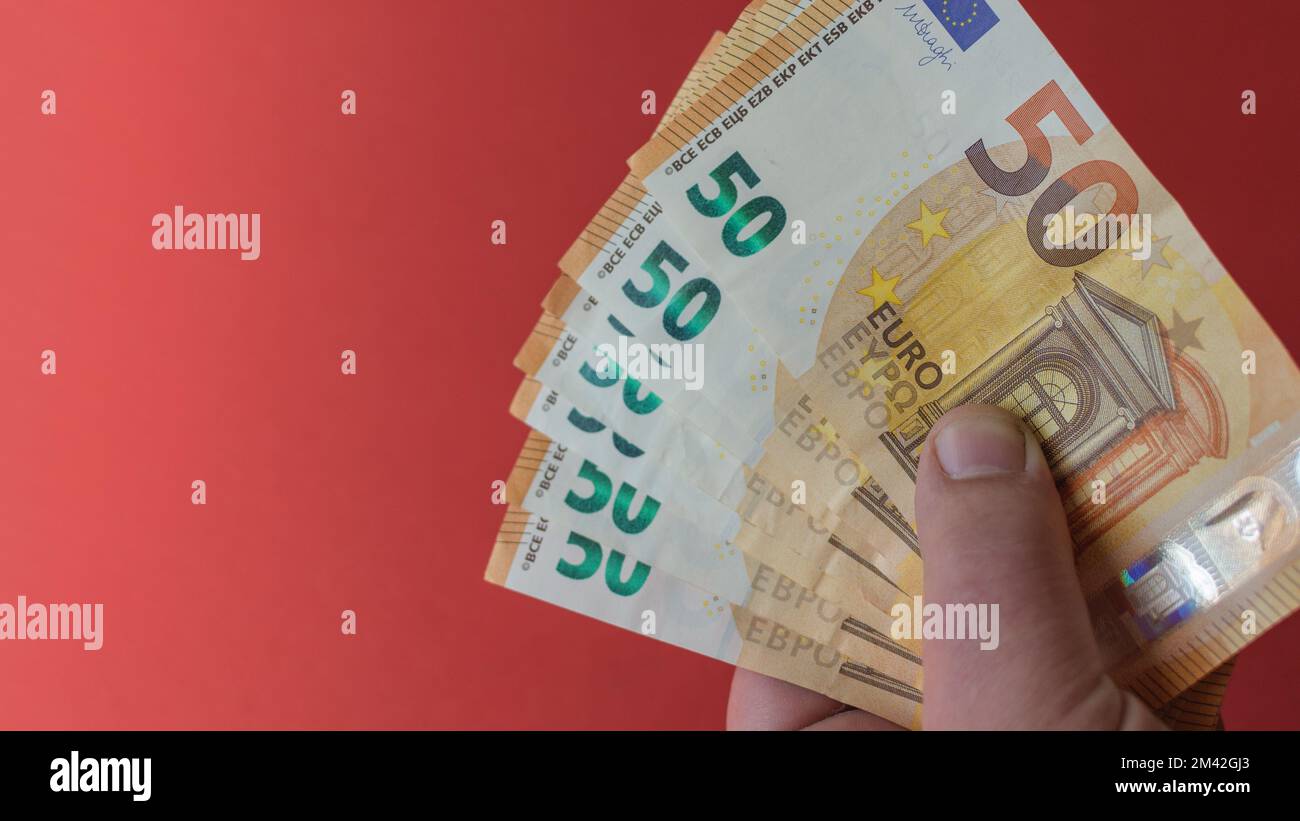 Hand holds out banknotes of 50 euros. Cash payment. Red background ...