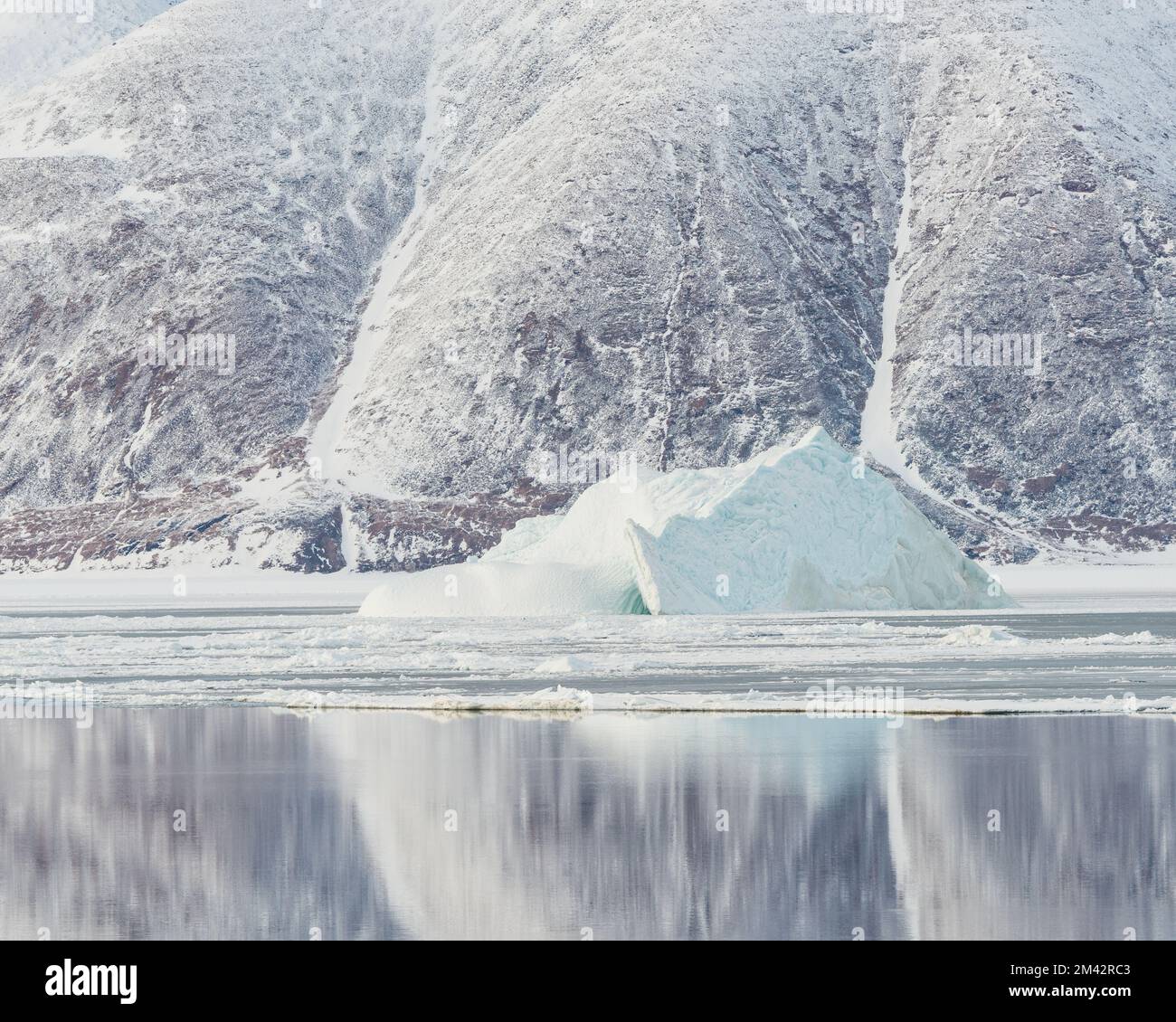 Iceberg reflected on water in front of mountain, Greenland Stock Photo ...