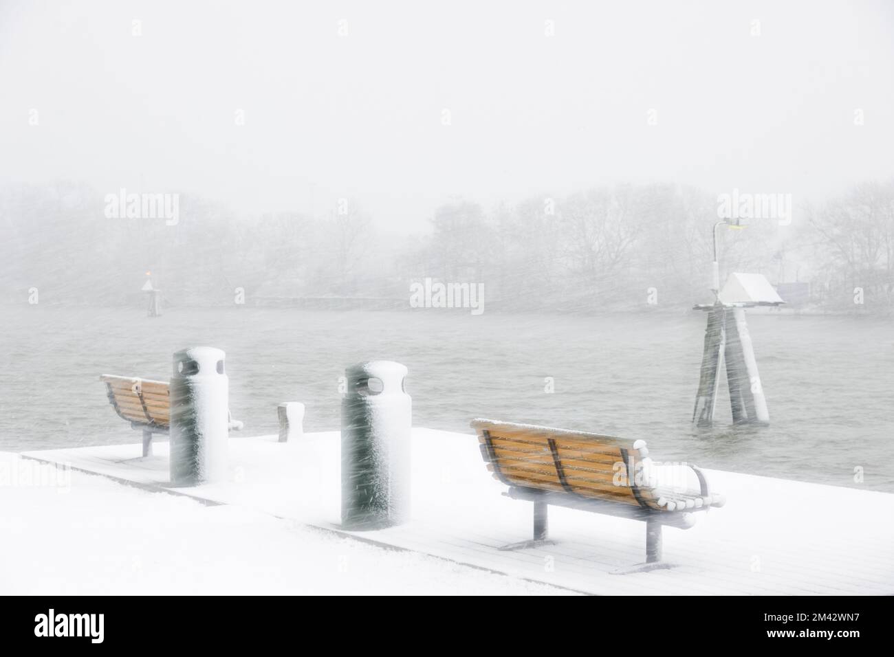 Snow falling on benches at the edge of a river Stock Photo - Alamy