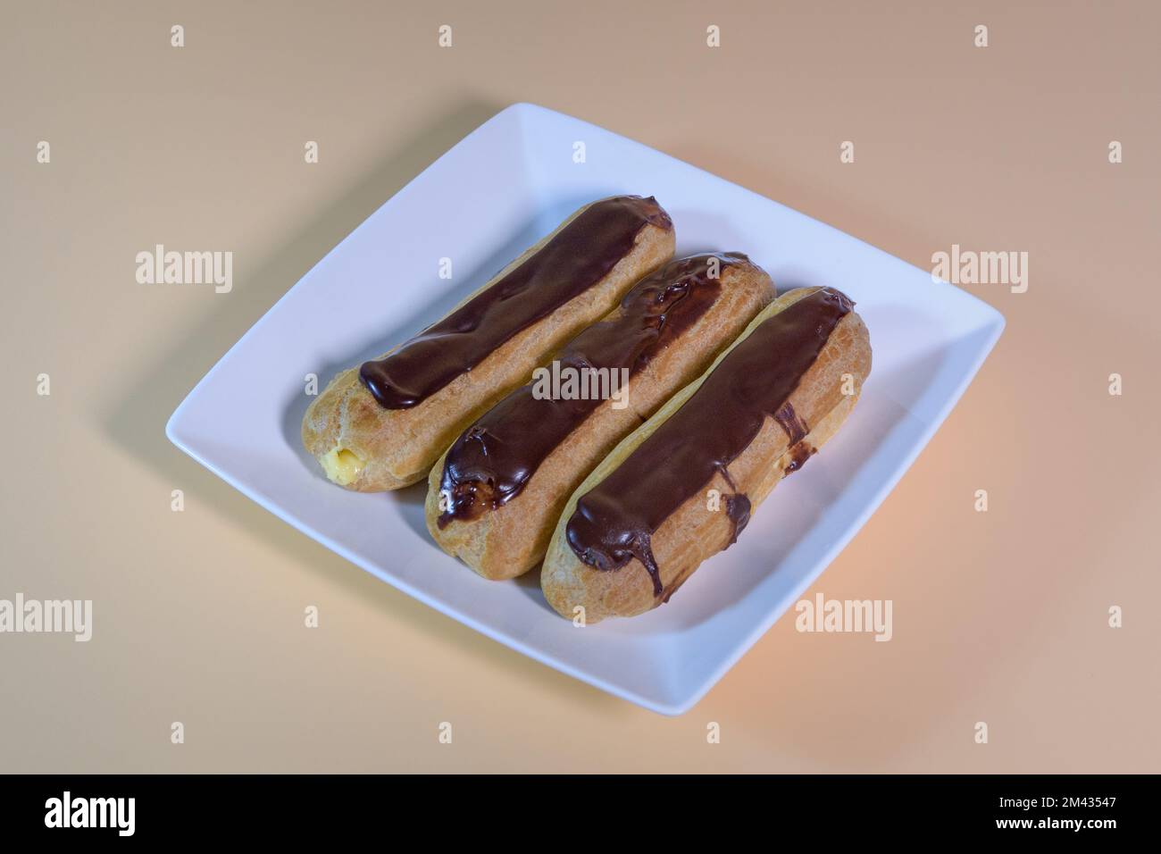 Three fresh eclairs on a white corner plate. On a beige background ...