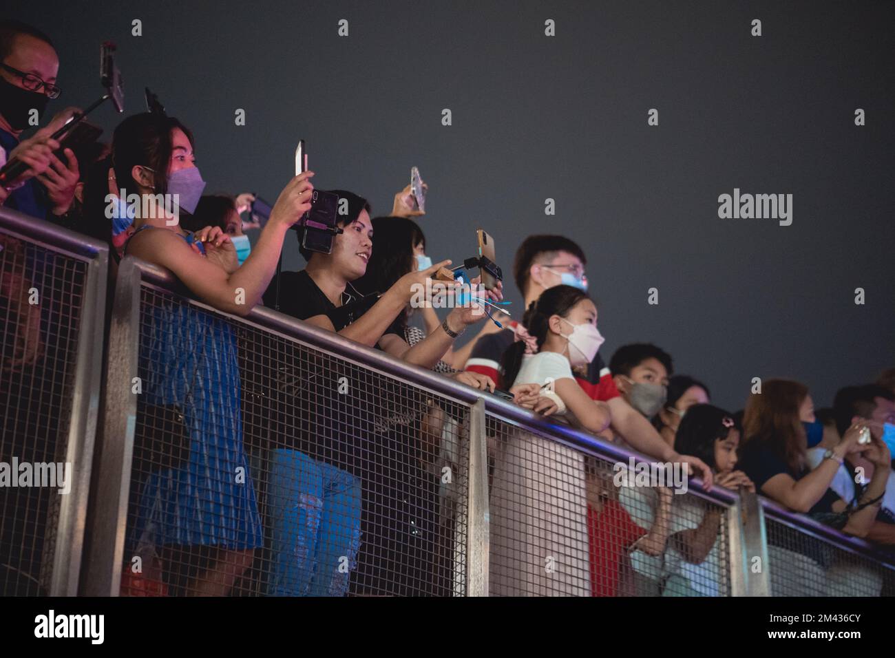 A concert crowd wearing faces masks standing behind the crowd control ...