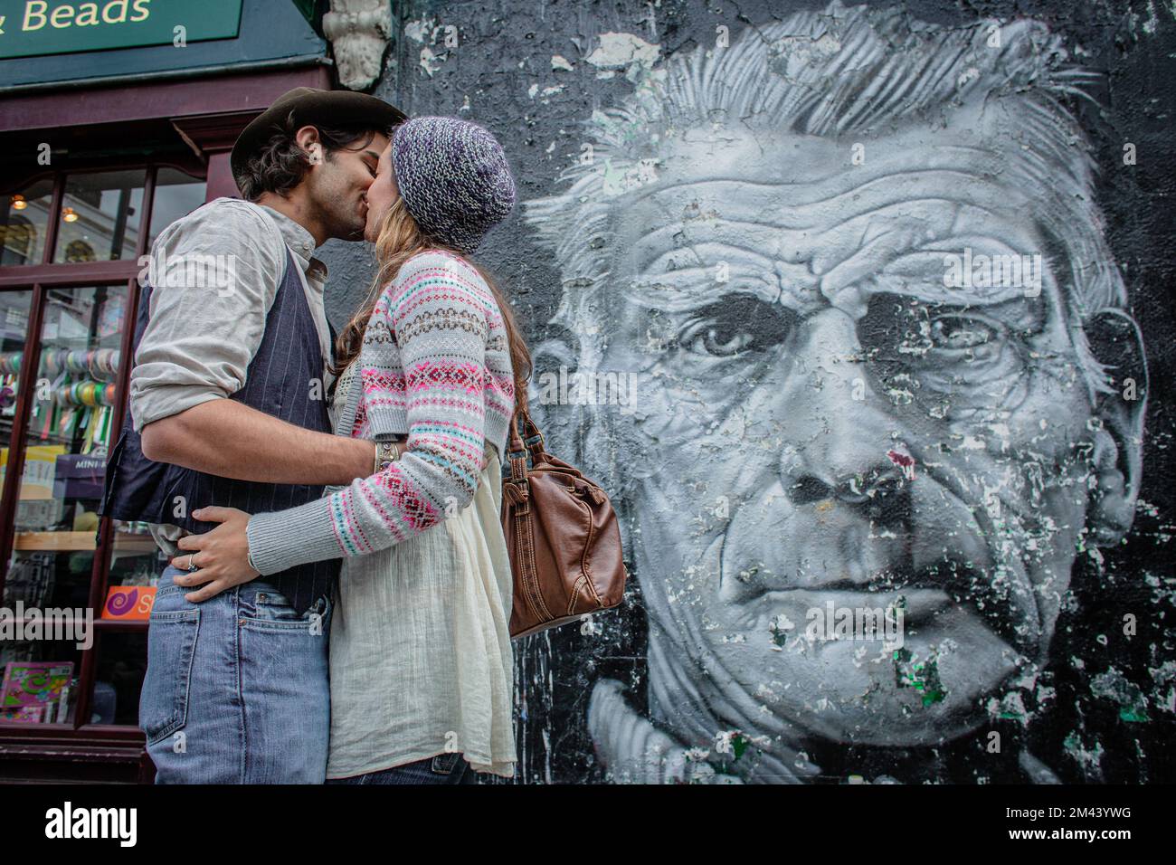 Young adult caucasian couple kissing in front a Samuel Becket Graffiti ...
