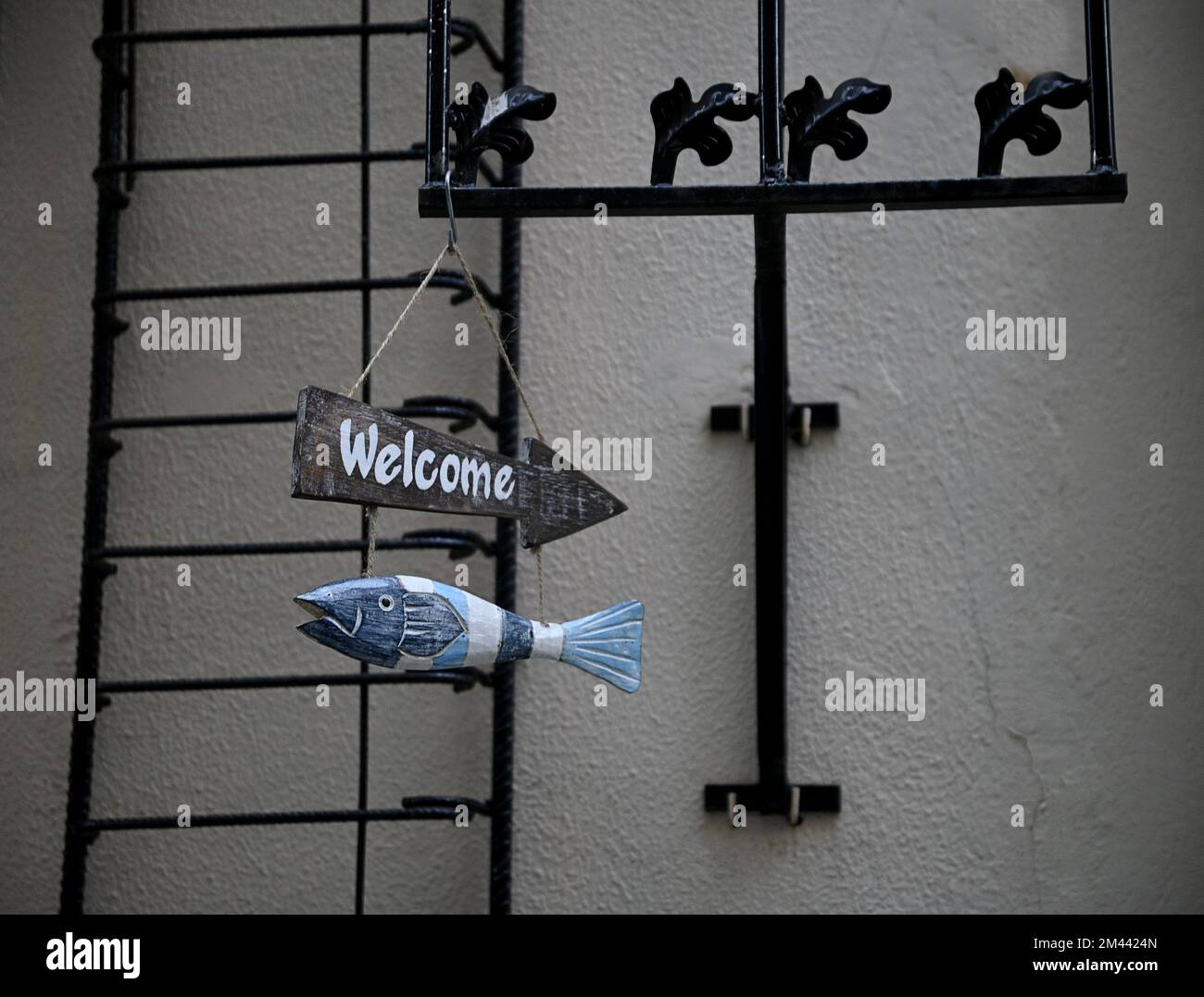 Hand painted fish welcome sign hanging from a metal wall garden trellis ...