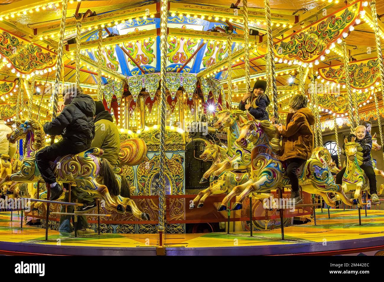Brightly coloured fairground carousel with galloping ponies. At ...