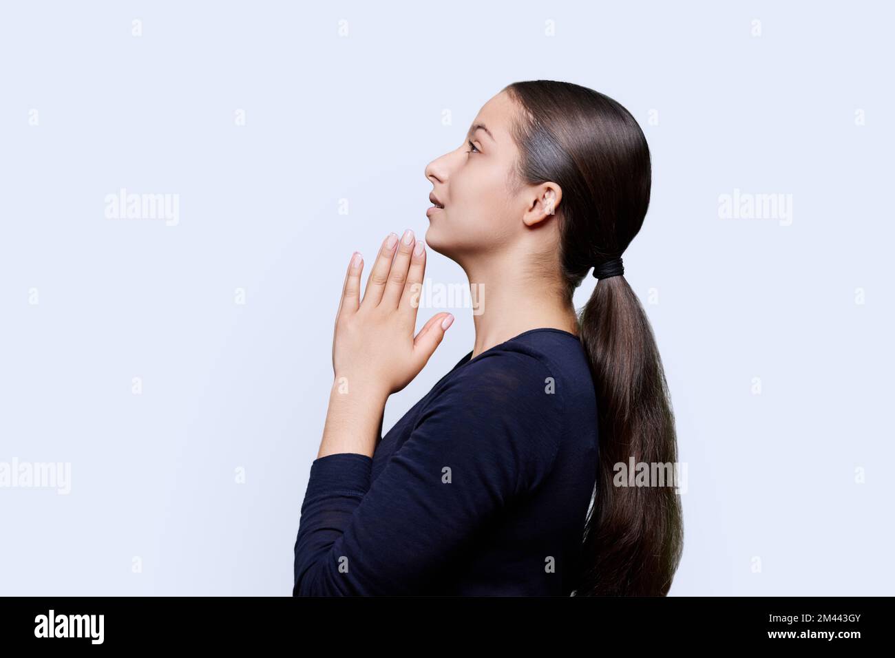 Young female pleading, holding hands in prayer on white background ...