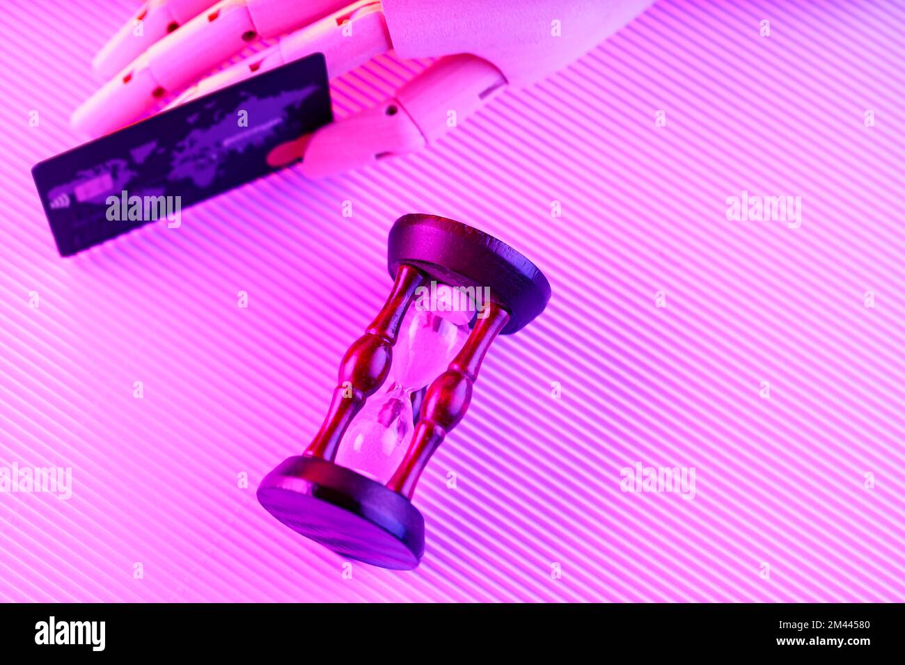 Bank card in an artificial hand. Credit card and hourglass in neon ...