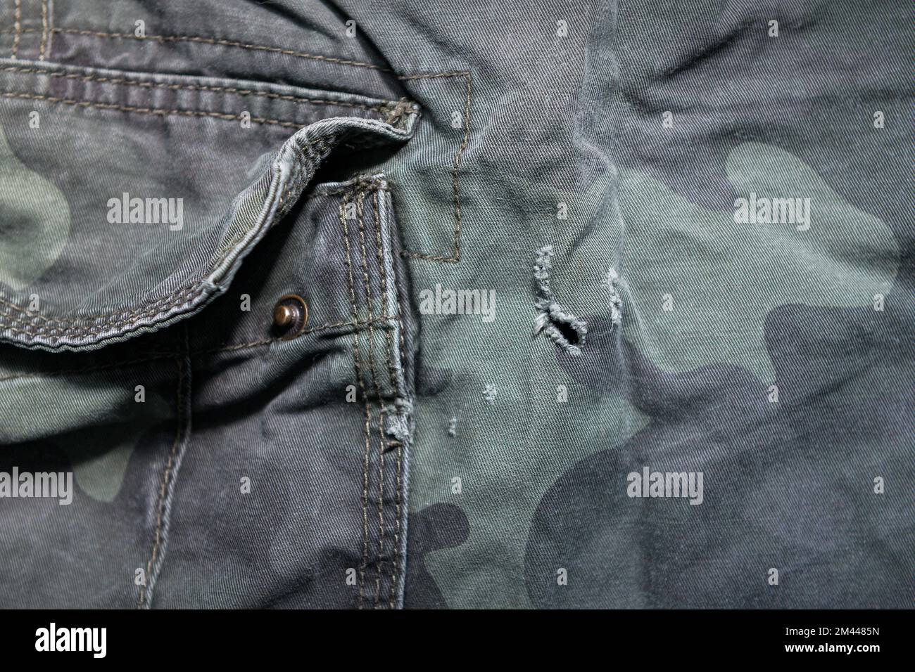 Damaged military uniform. Hole in camouflage fabric Stock Photo - Alamy