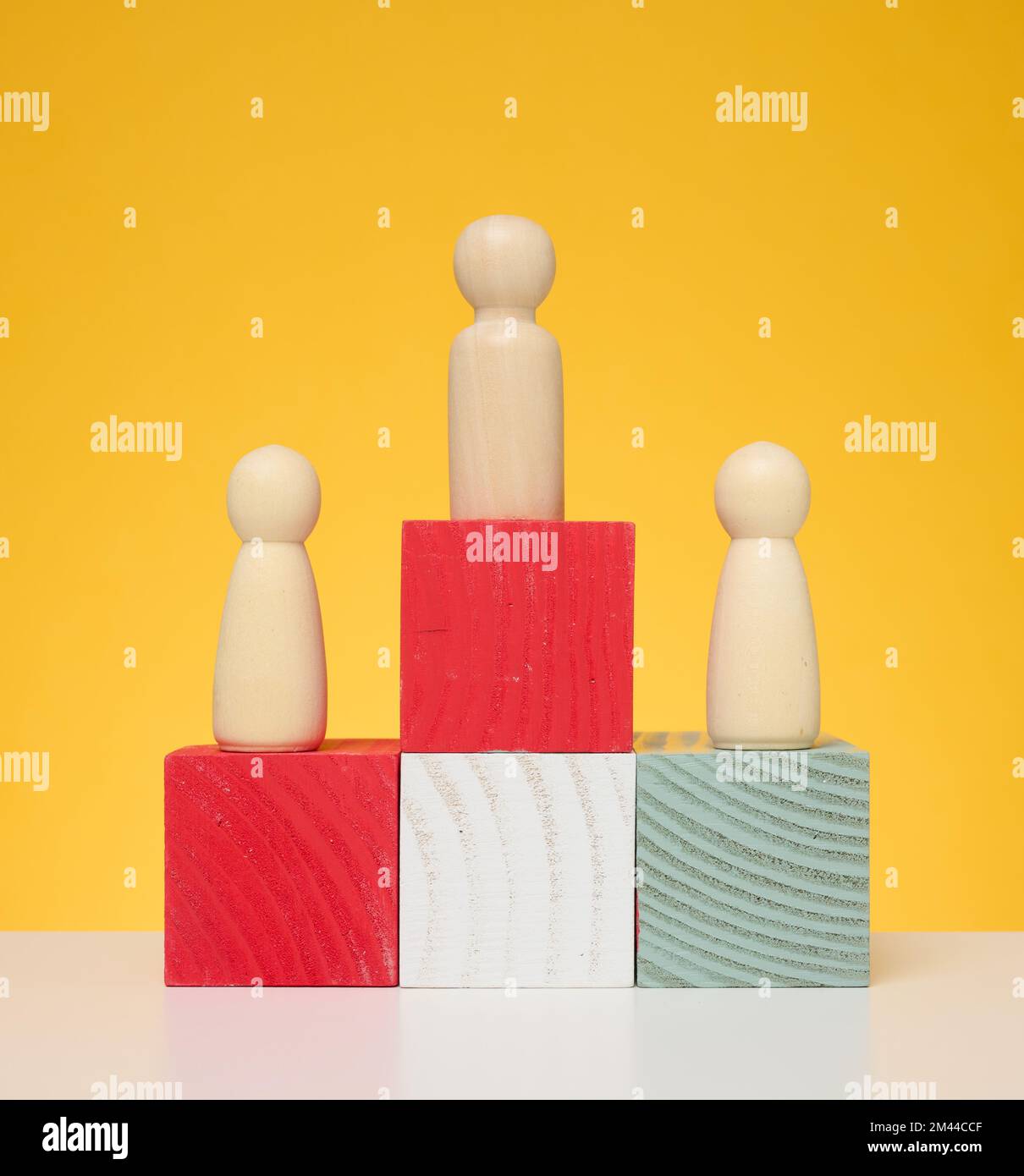 Wooden figures of men stand on a pedestal of their cubes on a yellow ...