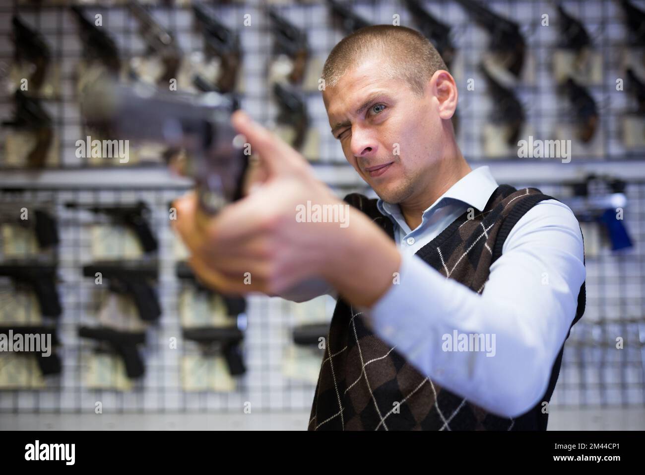 Interested man imitating aiming with pistol in gun shop Stock Photo - Alamy