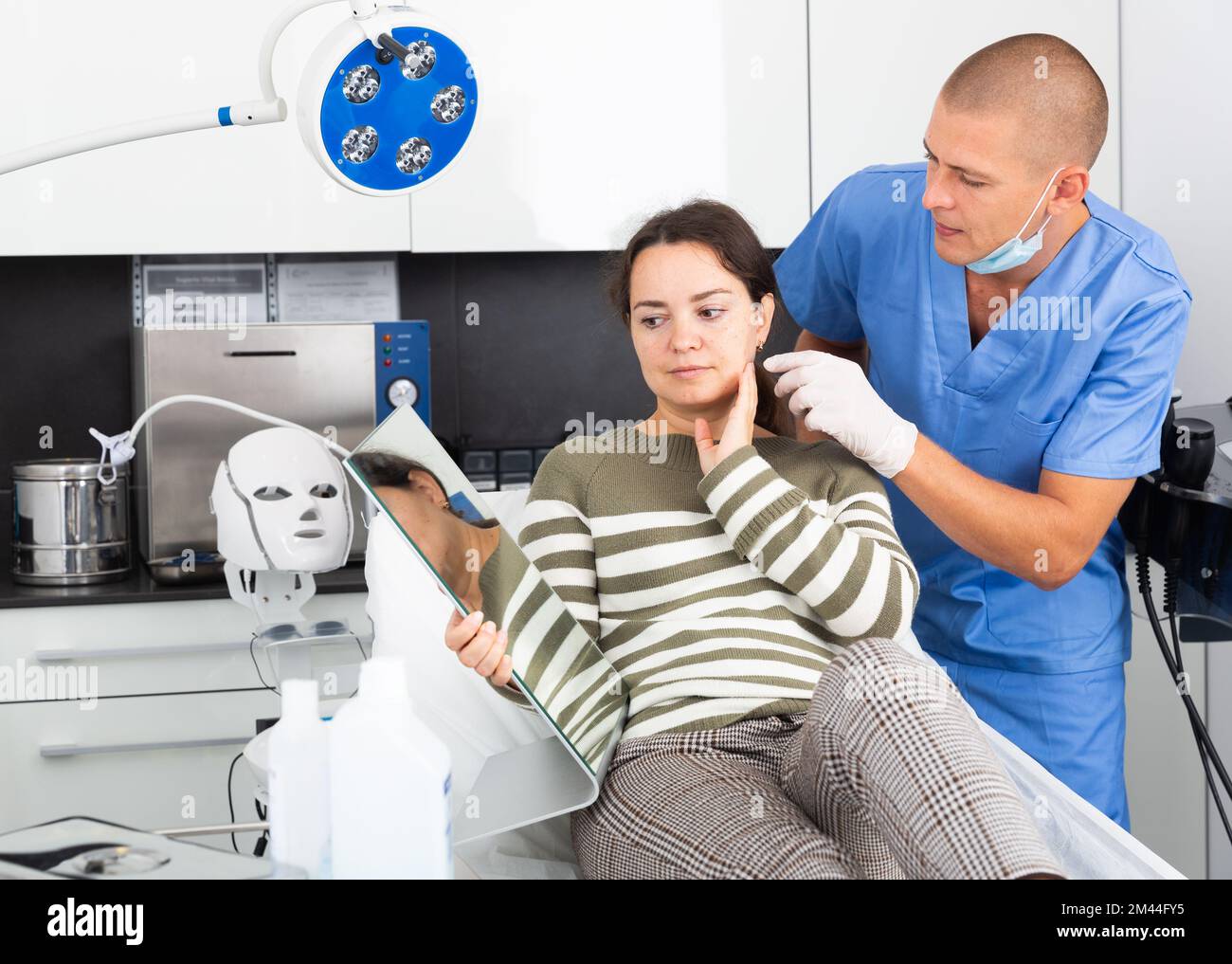 Cosmetologist examining female client face before procedure Stock Photo ...