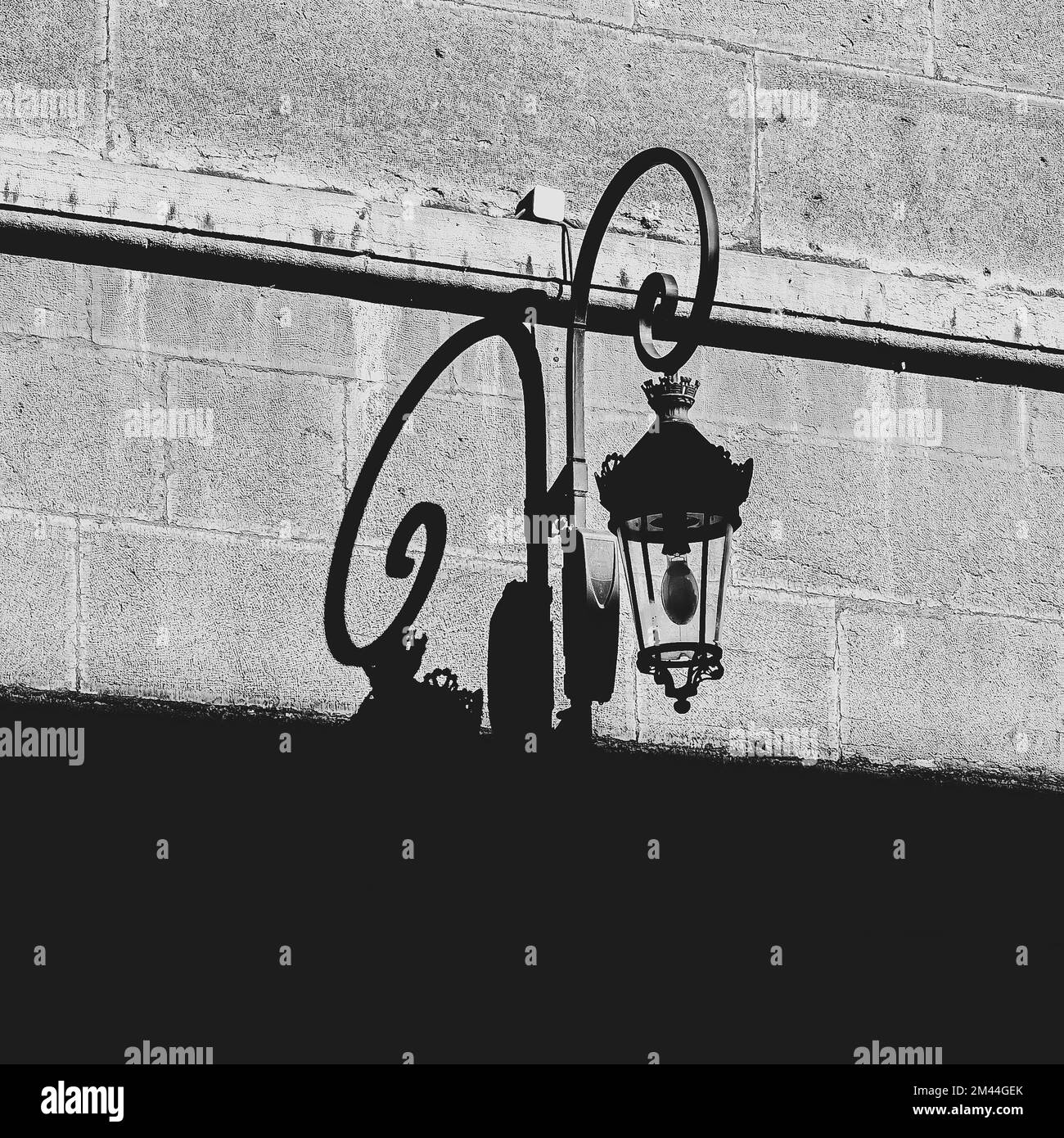 A grayscale of a street lamp casting its shadow on a wall captured in a ...