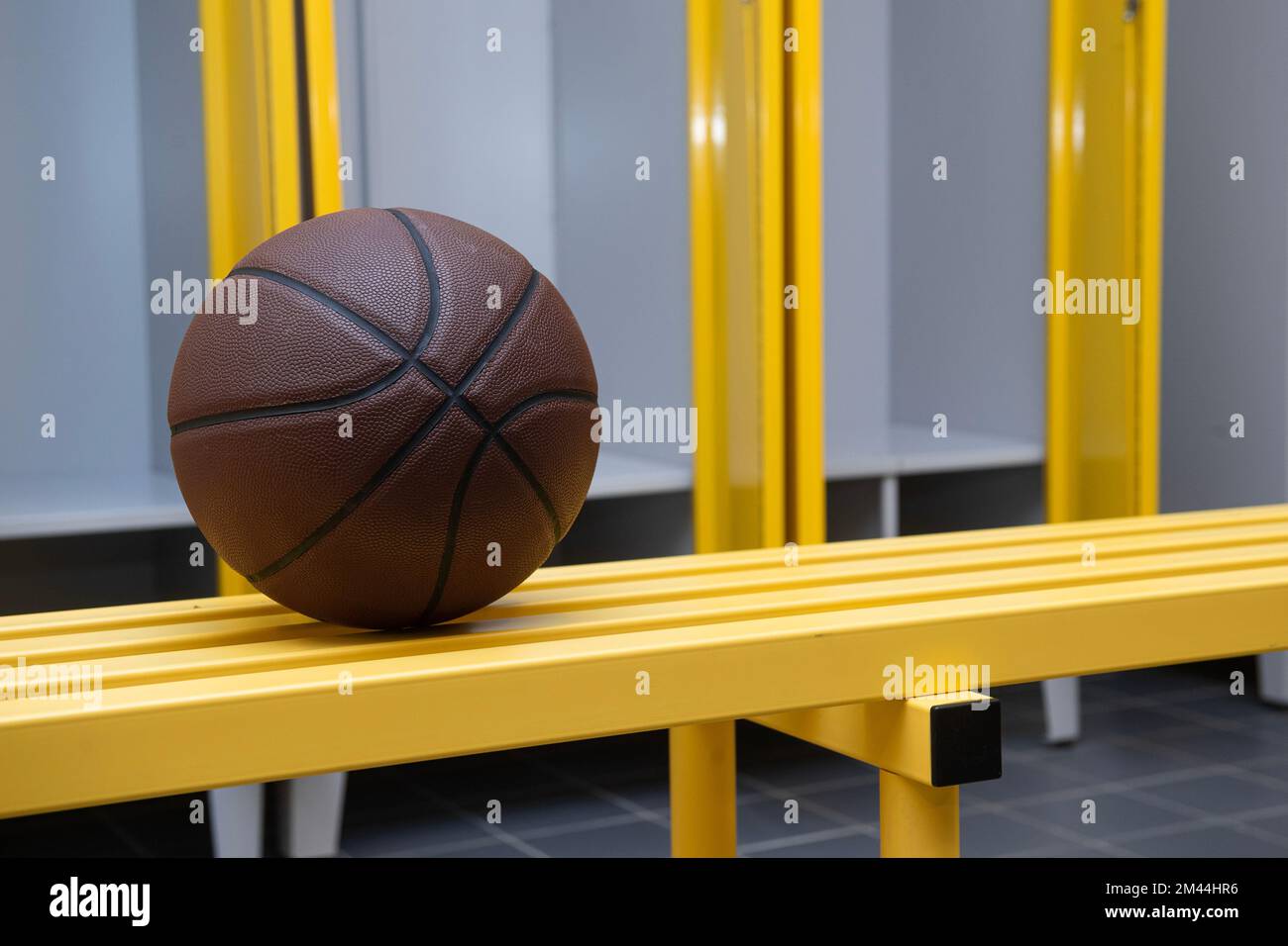 Brown basketball ball on yellow bench in locker room. Horizontal sport ...