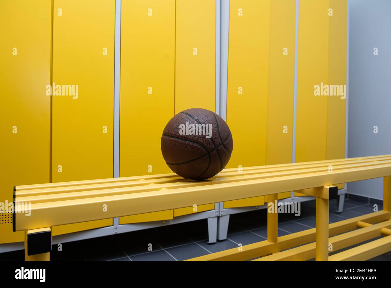 Brown basketball ball on yellow bench in locker room. Horizontal sport ...