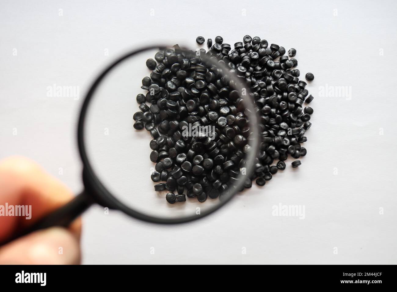 Photo of a raw plastic with a magnifying glass in hand on a white ...
