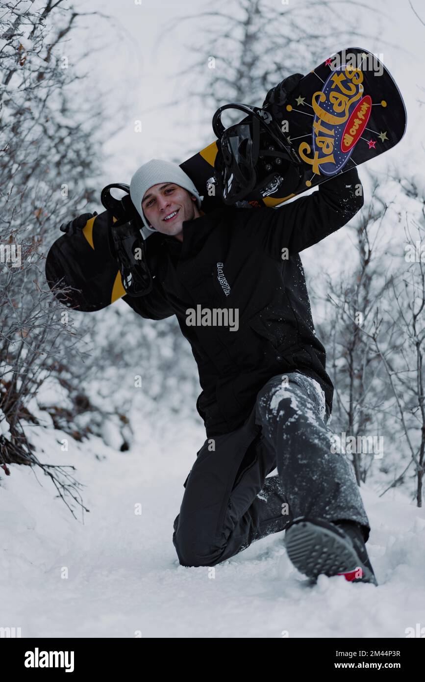 A young white man bending down in the snow holding a snowboard on his ...