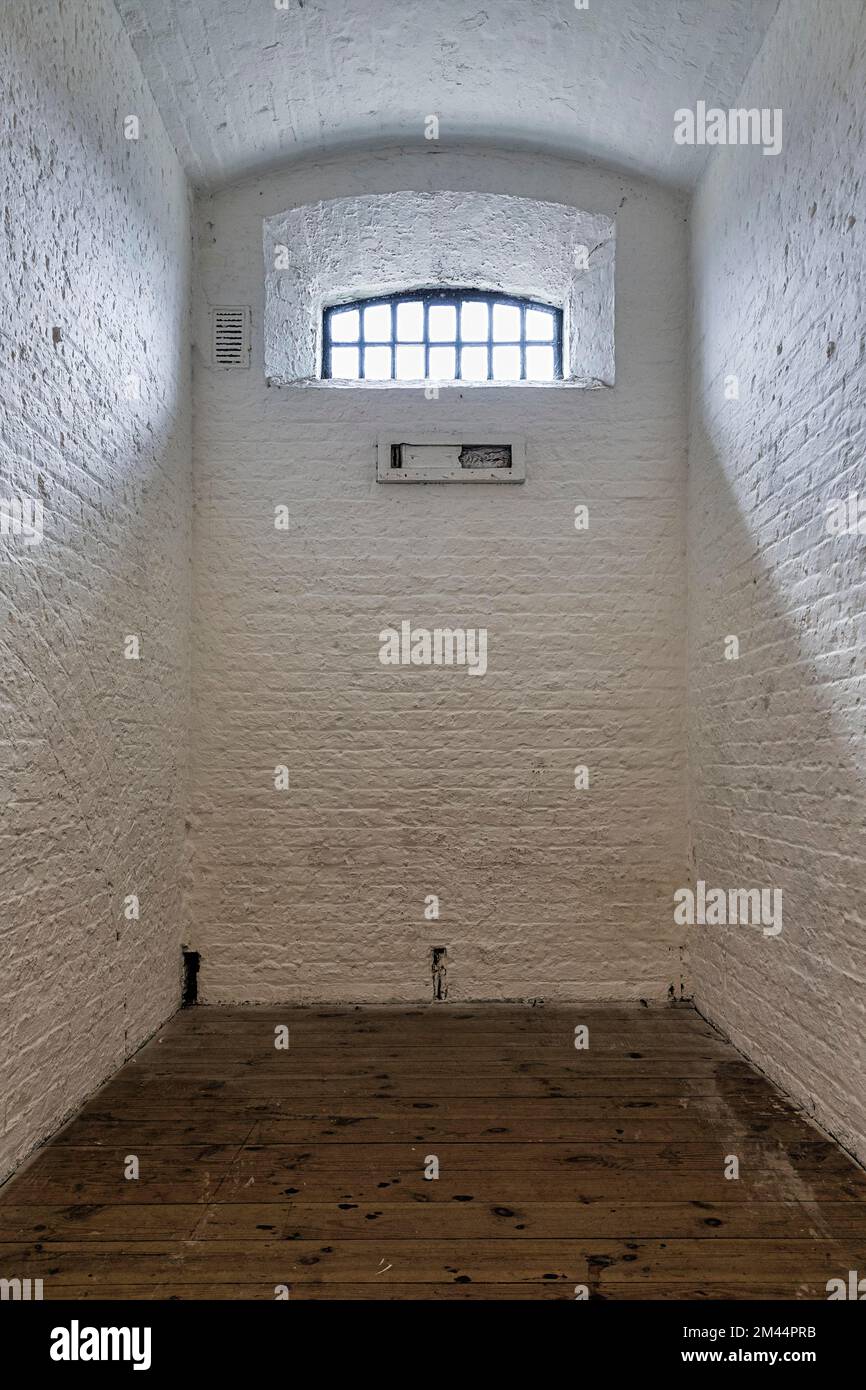 Cramped, restored prison cell, light streaming in through barred window ...