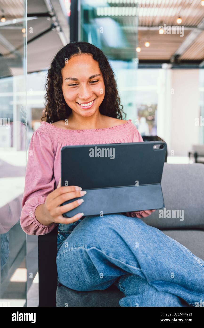 Hispanic university student woman smiling and using a tablet sitting ...