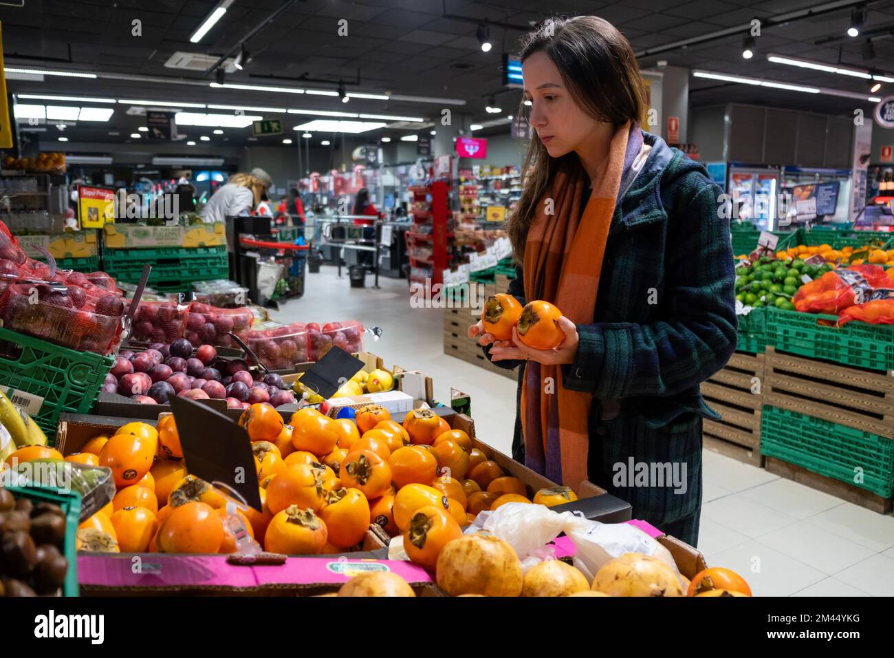 Young latin woman choosing fruits in a grocery store. Persimmon fruit ...
