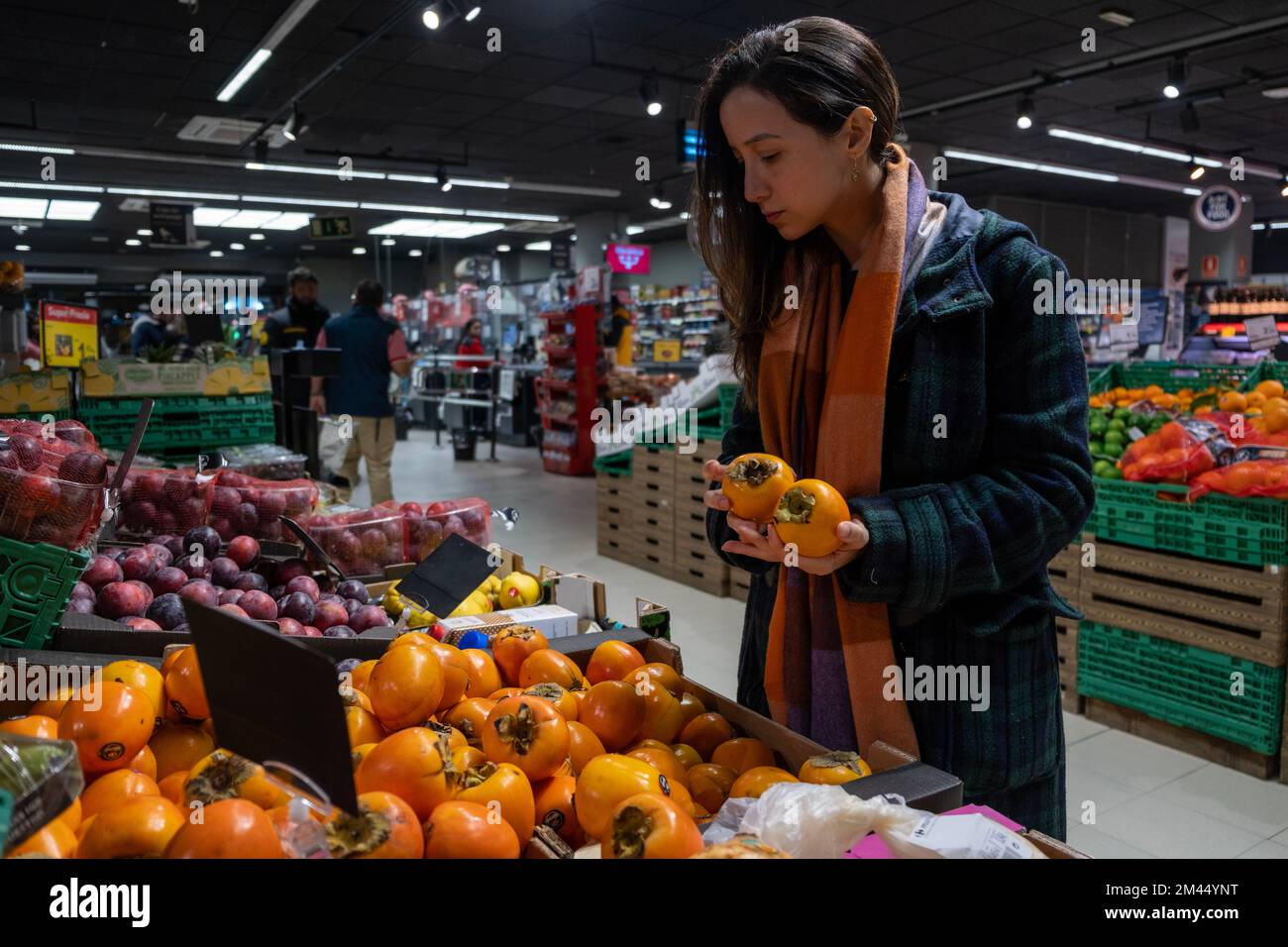 Young latin woman choosing fruits in a grocery store. Persimmon fruit ...