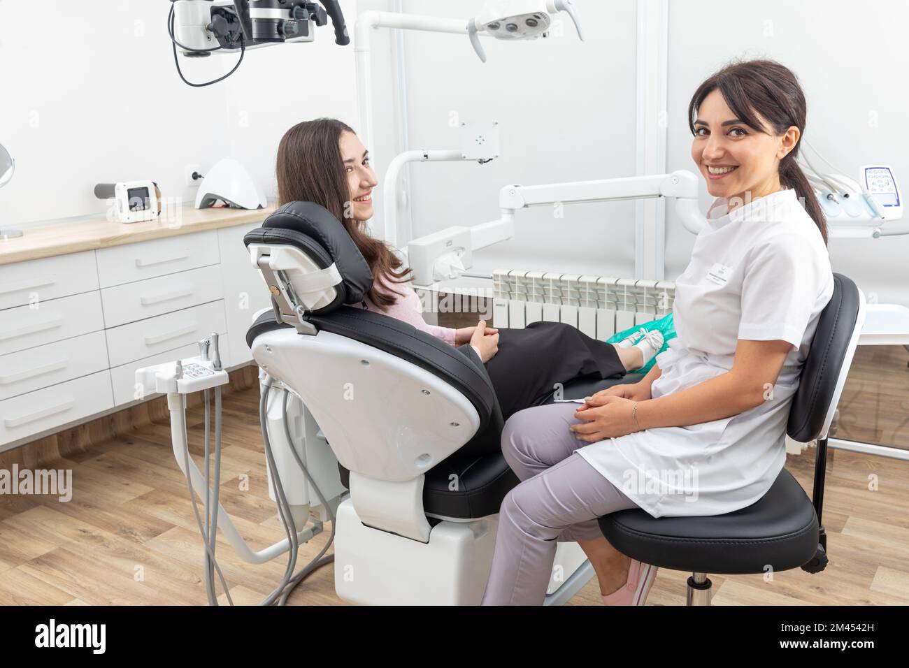Female dentist talking to a young patient during appointment in modern ...