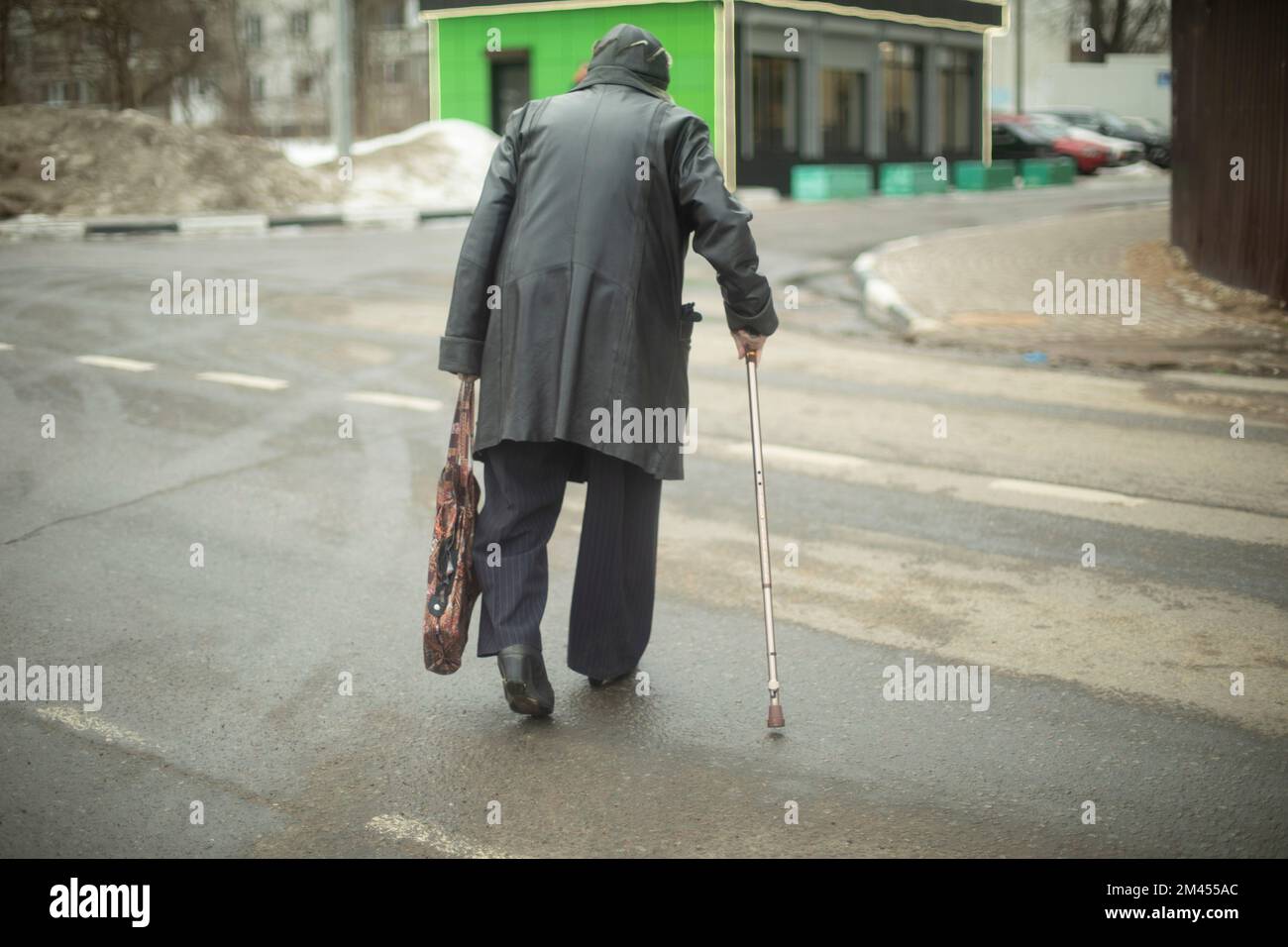 Old Woman Walks Down Road In Black Jacket Pensioner In Russia On