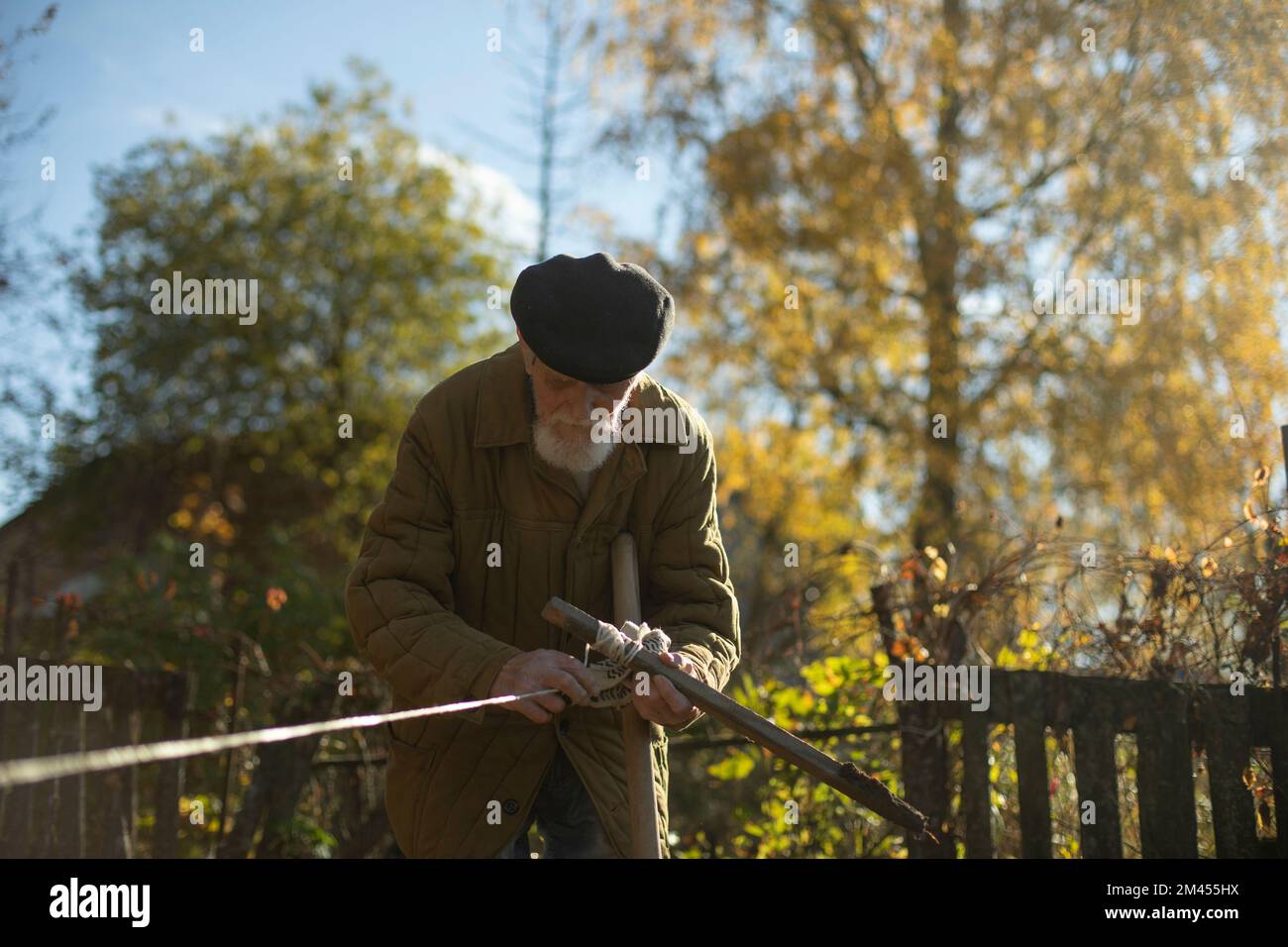 Old man measures earth. Grandfather pulls rope in garden. Old man ...