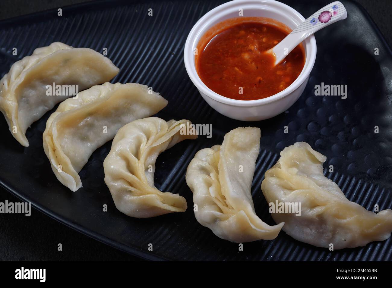 Picture of steamed chicken stuffed momo with sauce served in a black ...