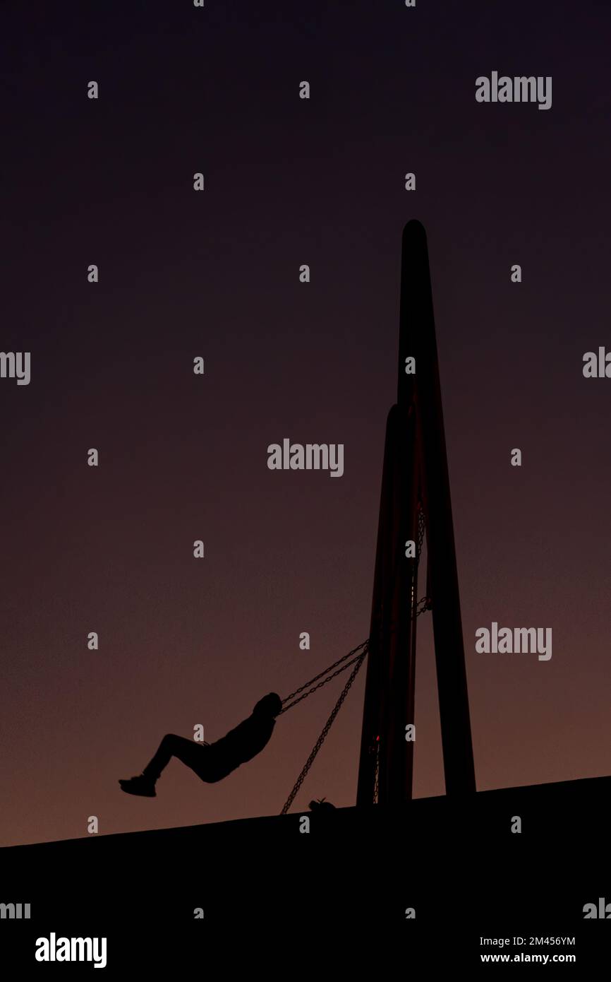 man swinging with the sunset in the background at night only shadow by ...