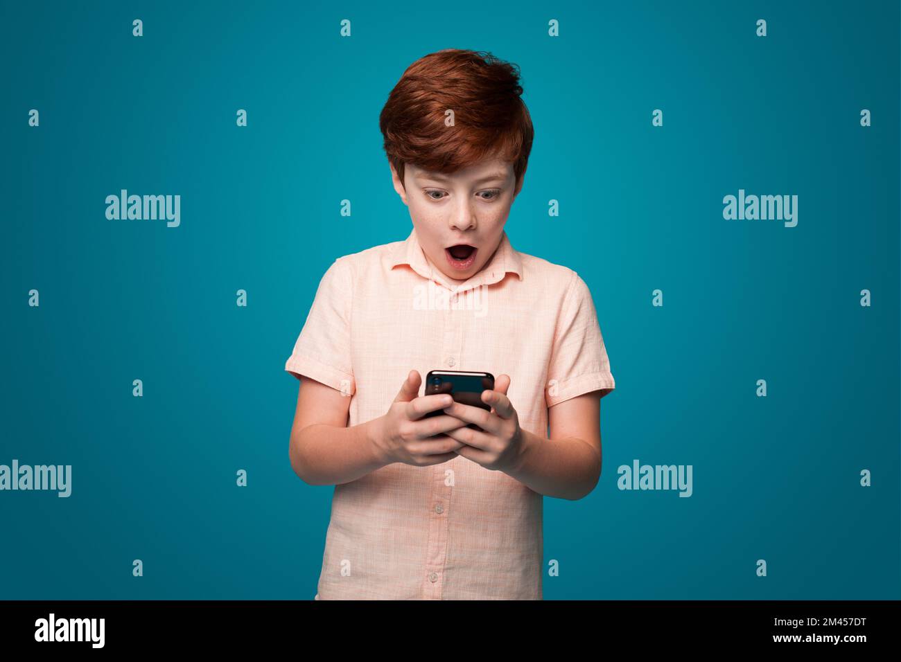 Little caucasian kid looking at the screen of the phone shocked with ...