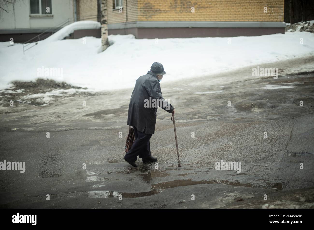 Old Woman Walks Down Road In Black Jacket Pensioner In Russia On