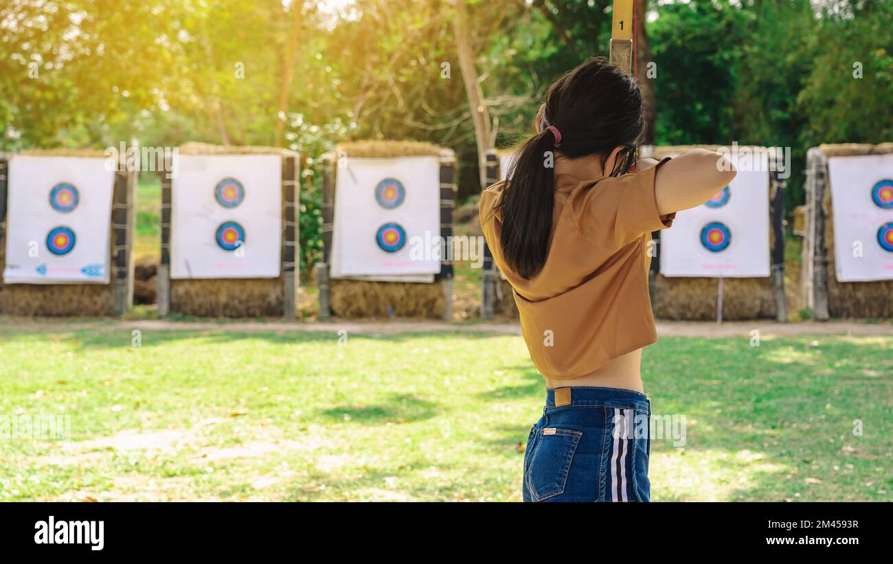 Back view of Asian girl wear face mask aims archery bow and arrow to ...