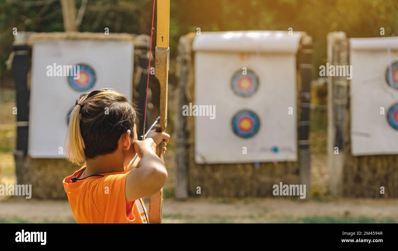Back view of Asian boy wear face mask aims archery bow and arrow to ...