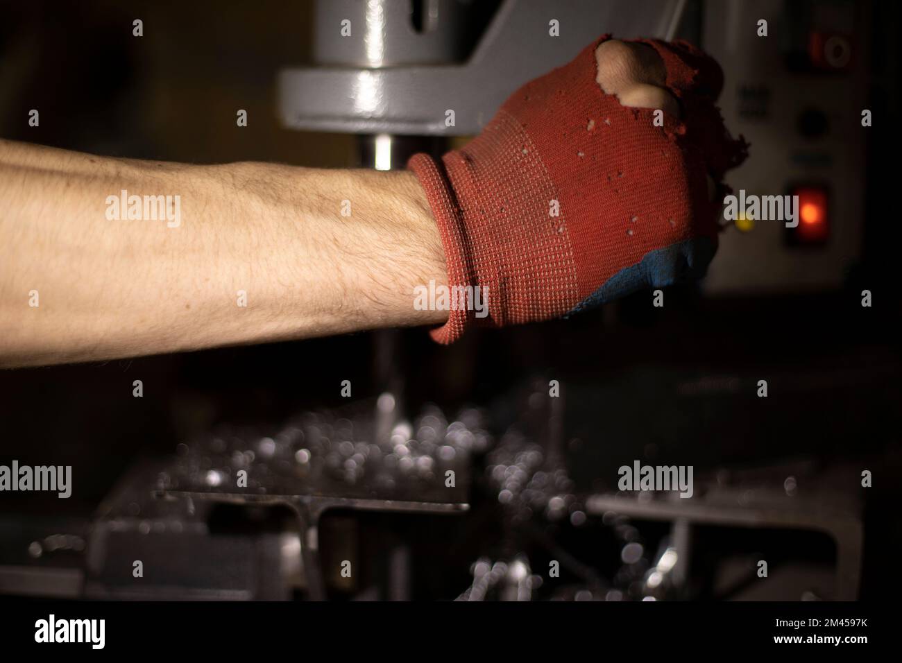 Gloved hand drills part. Worker's hand in garage. Red glove with hole ...