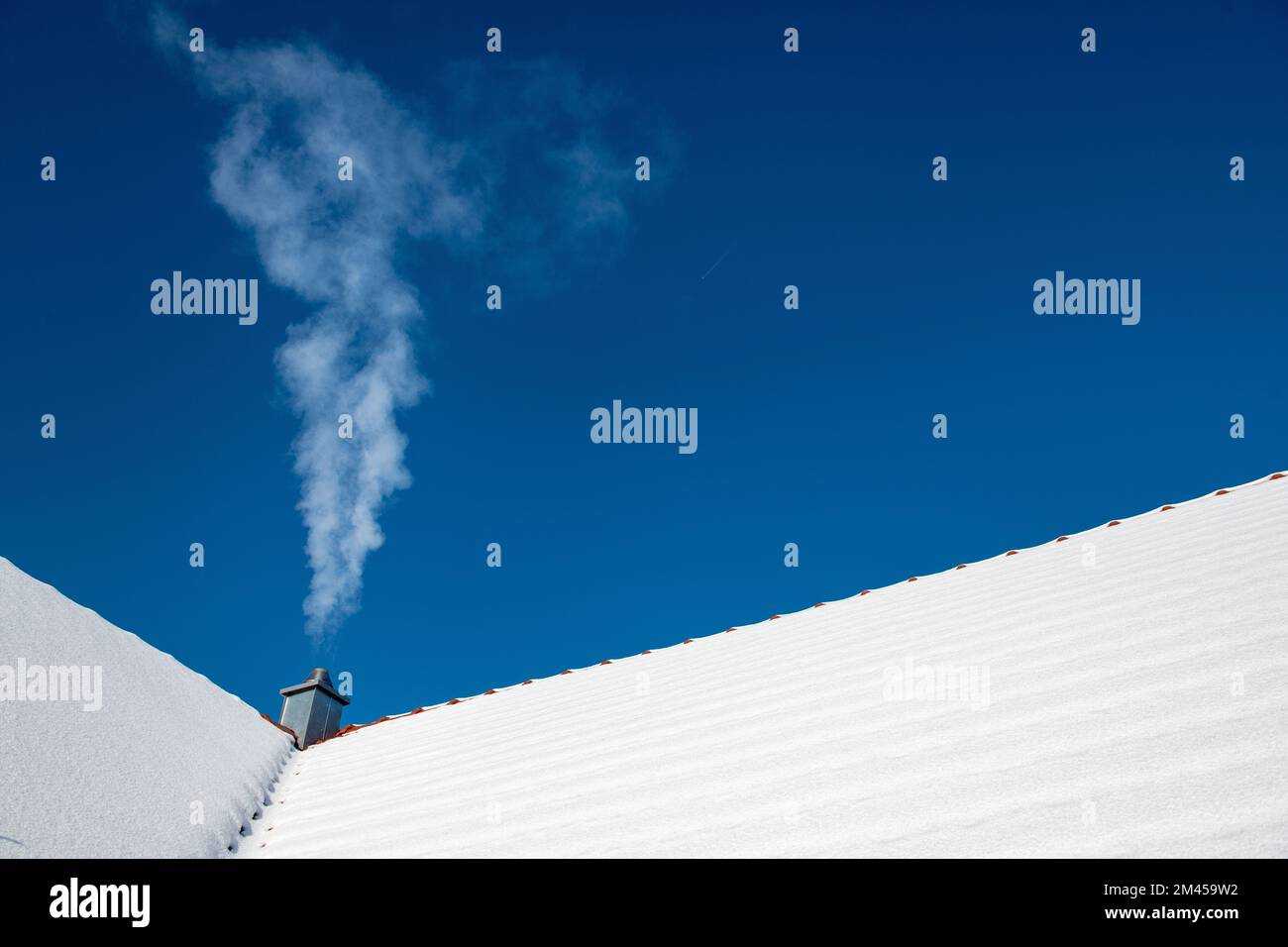 chimney smokes in the winter cold with a bright blue sky and sunshine ...