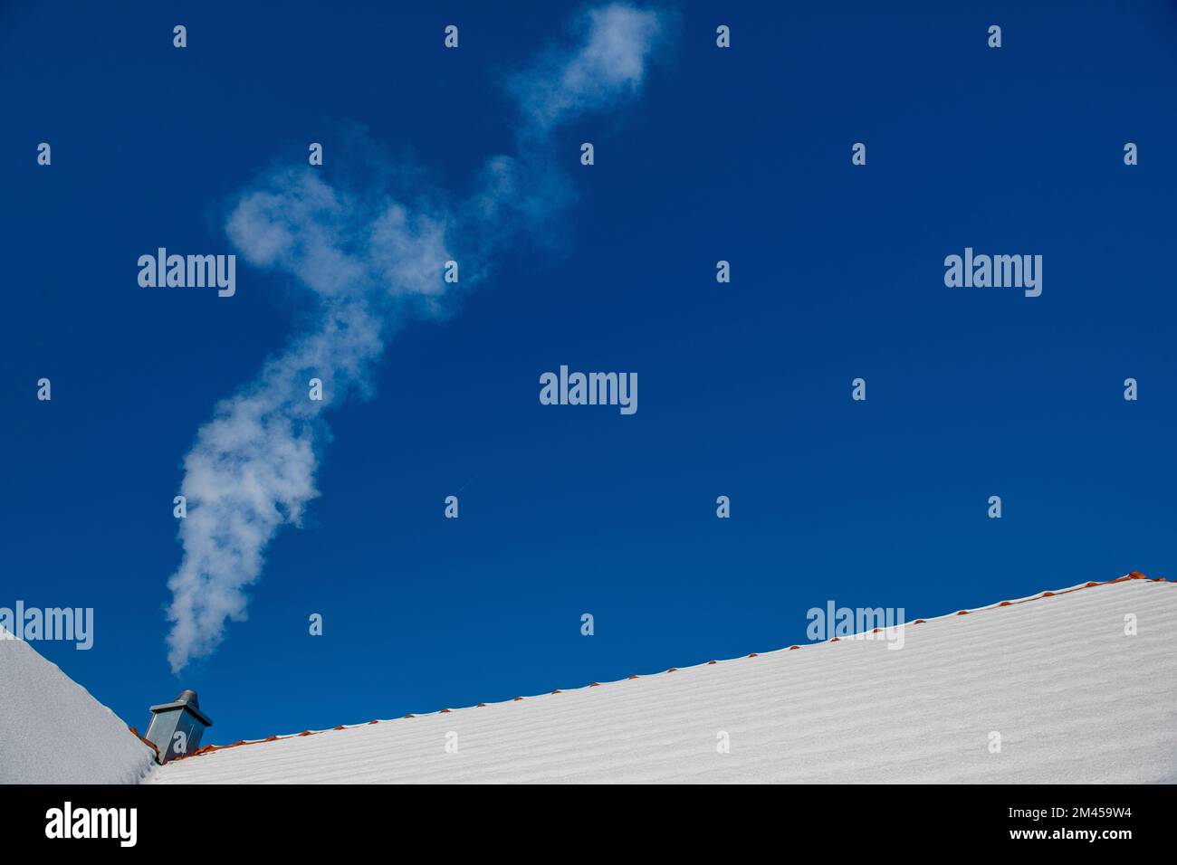 chimney smokes in the winter cold with a bright blue sky and sunshine ...