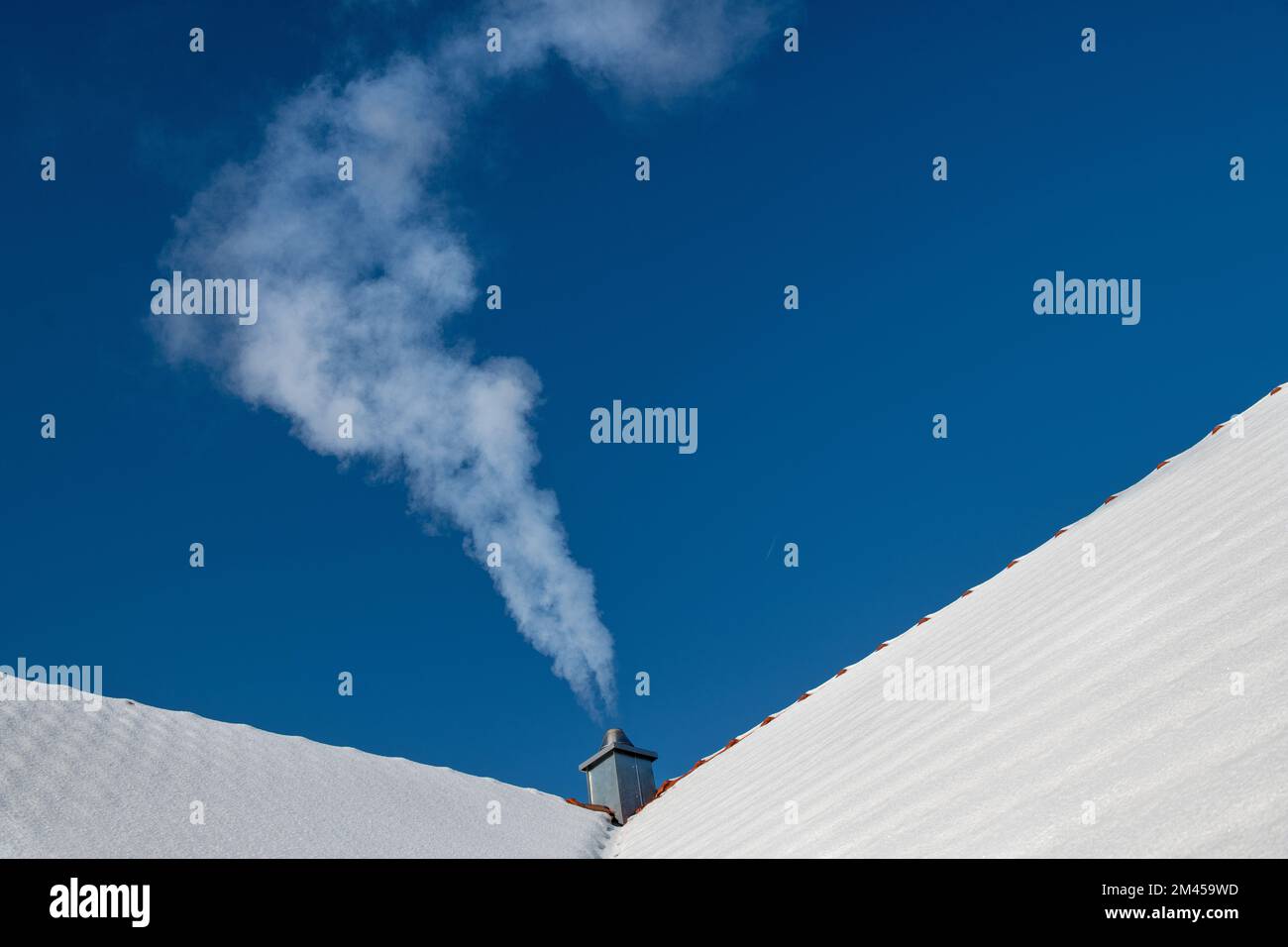 chimney smokes in the winter cold with a bright blue sky and sunshine ...