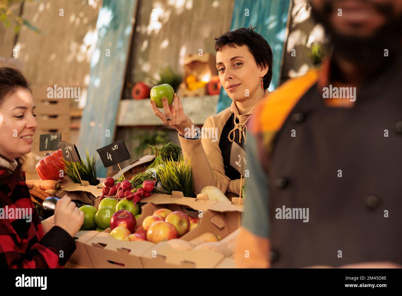 Young female farmer showing various organic fruits to customers at ...