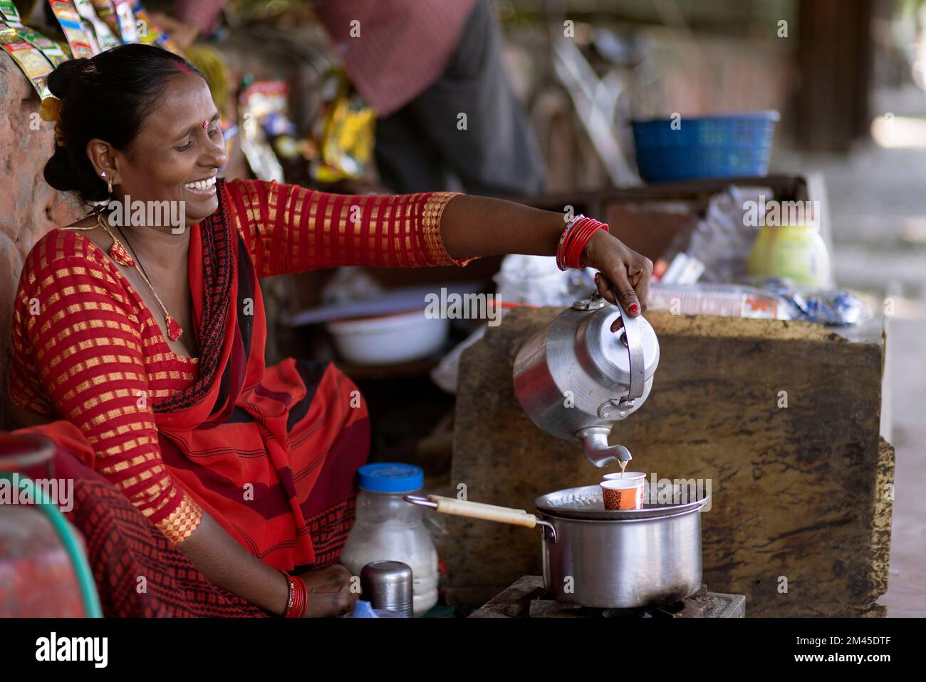 Female vendor pouring chai into cup for customer at a roadside stall ...