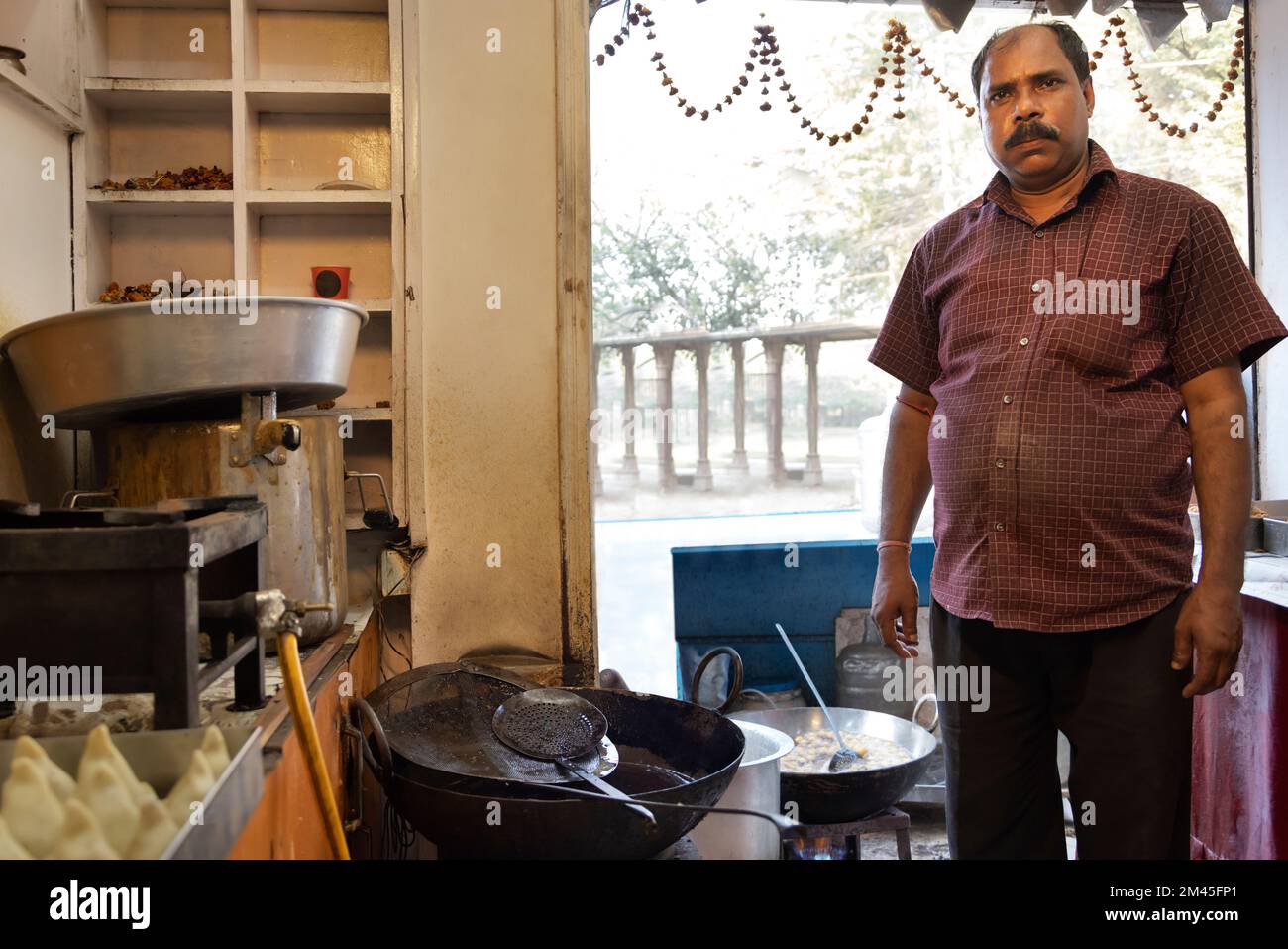 Owner of a sweet shop known as a Halwai standing in the kitchen of his ...