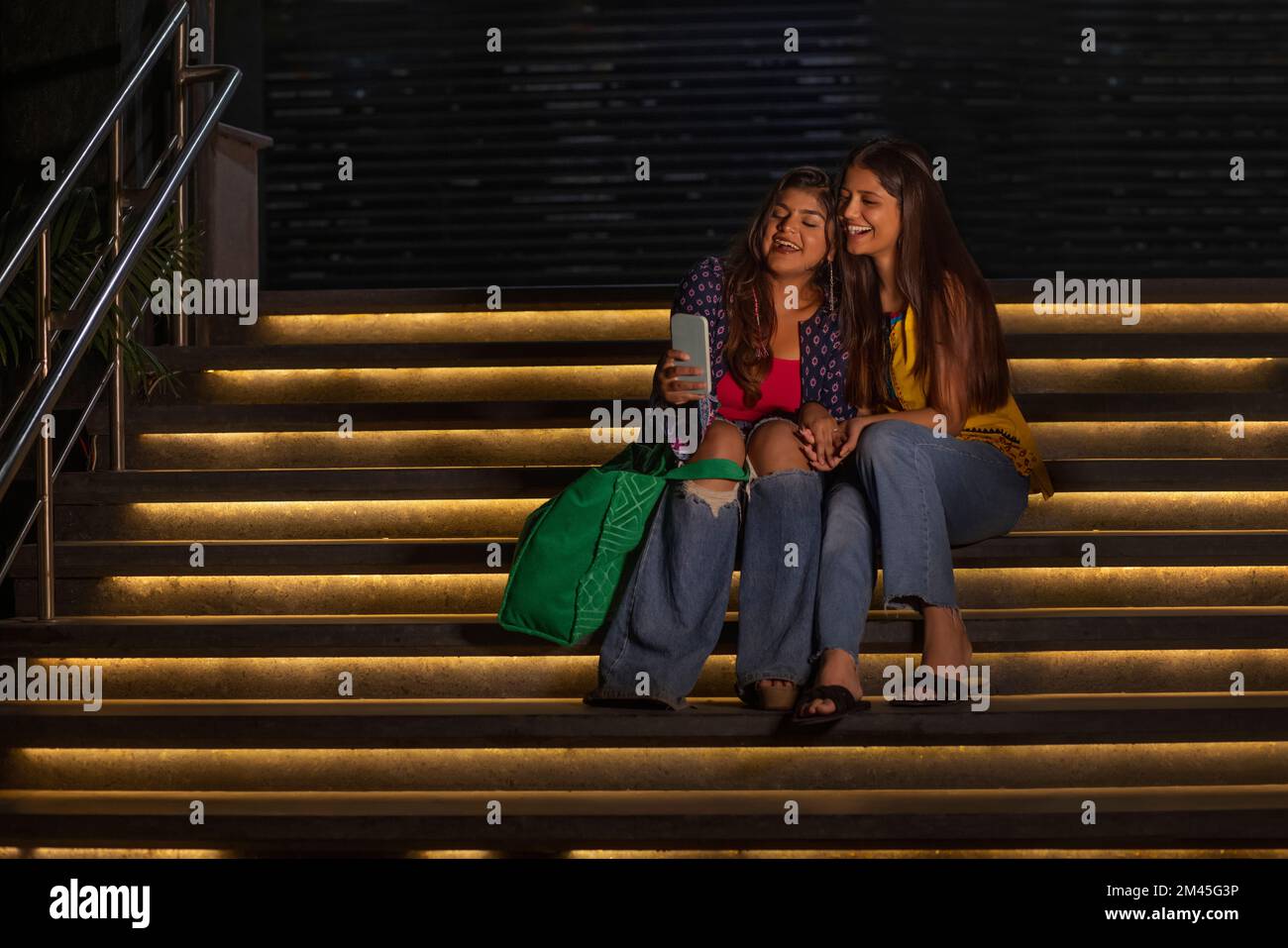 Two women sitting on steps and watching mobile phone Stock Photo - Alamy