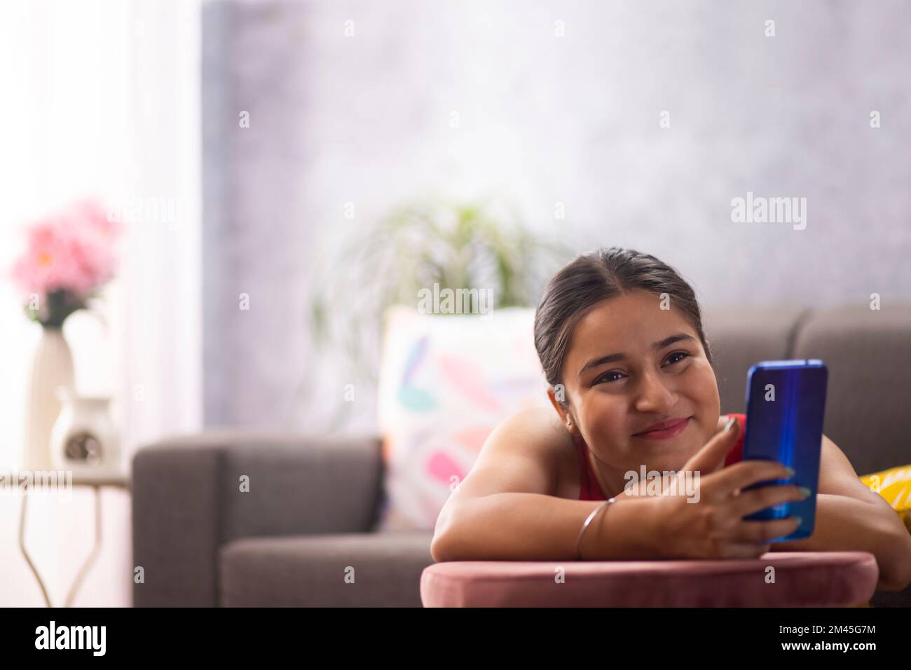 Happy teenage girl watching mobile phone in living room Stock Photo - Alamy