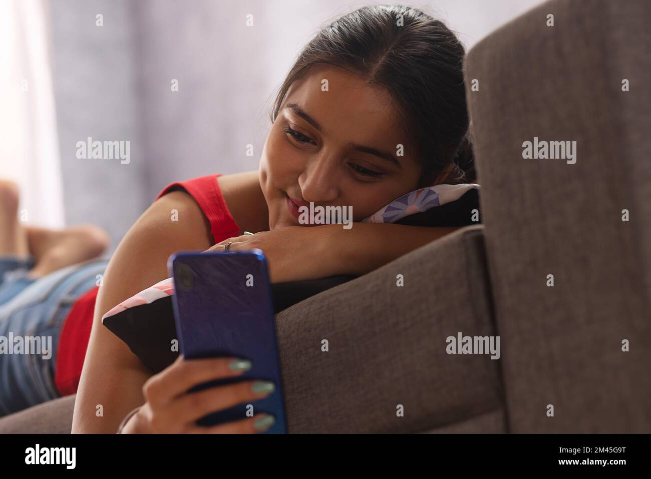 Teenage girl using mobile phone while lying down on sofa at home Stock ...