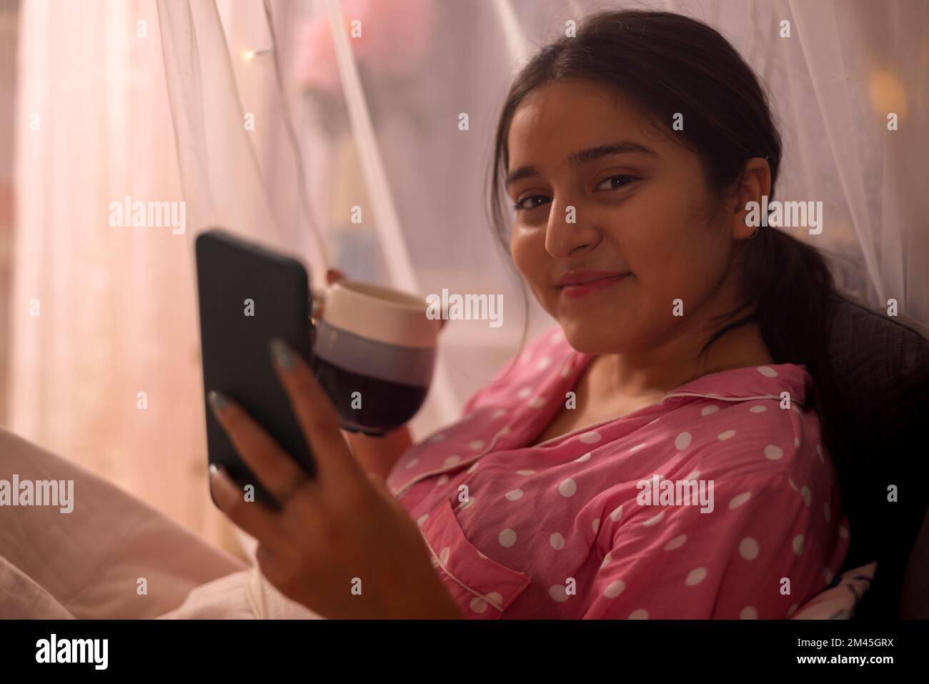Closeup portrait of a teenage girl using mobile phone with a cup of ...