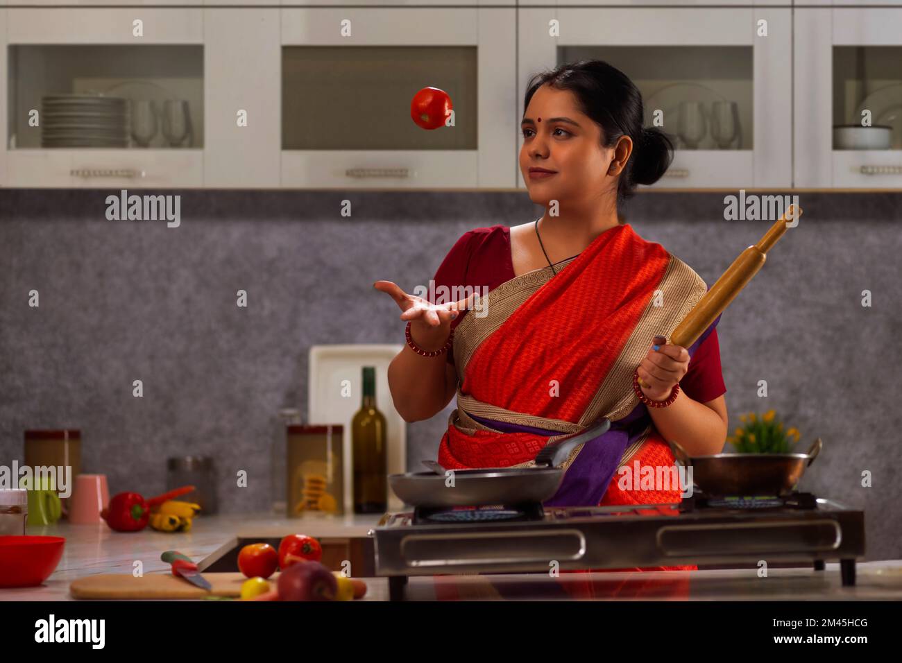 Woman with rolling pin in hand tossing tomato while cooking Stock Photo ...