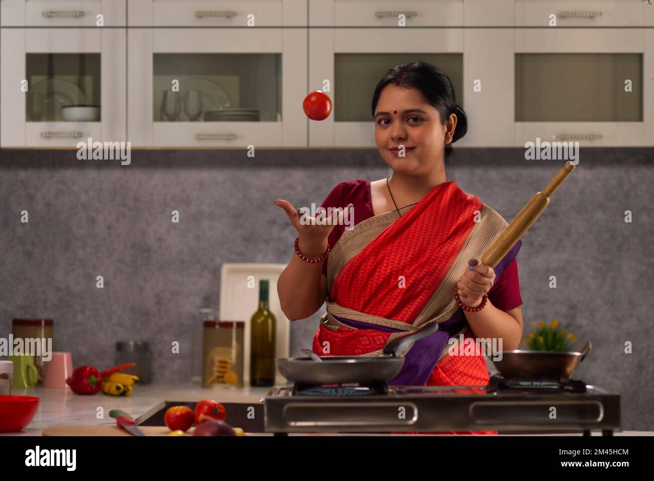 Woman with rolling pin in hand tossing tomato while cooking Stock Photo ...