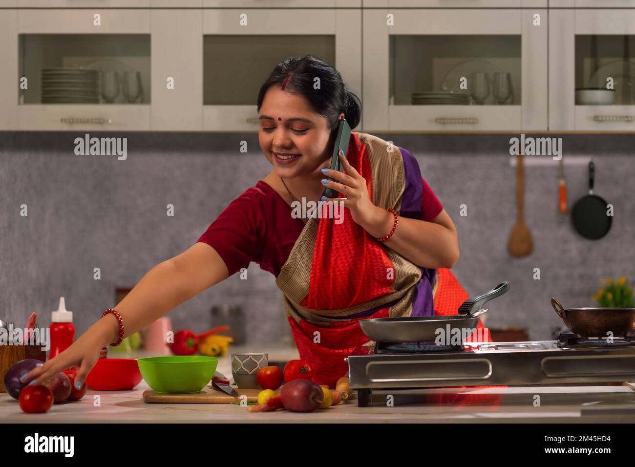 Woman talking on mobile phone while cooking in the kitchen Stock Photo ...