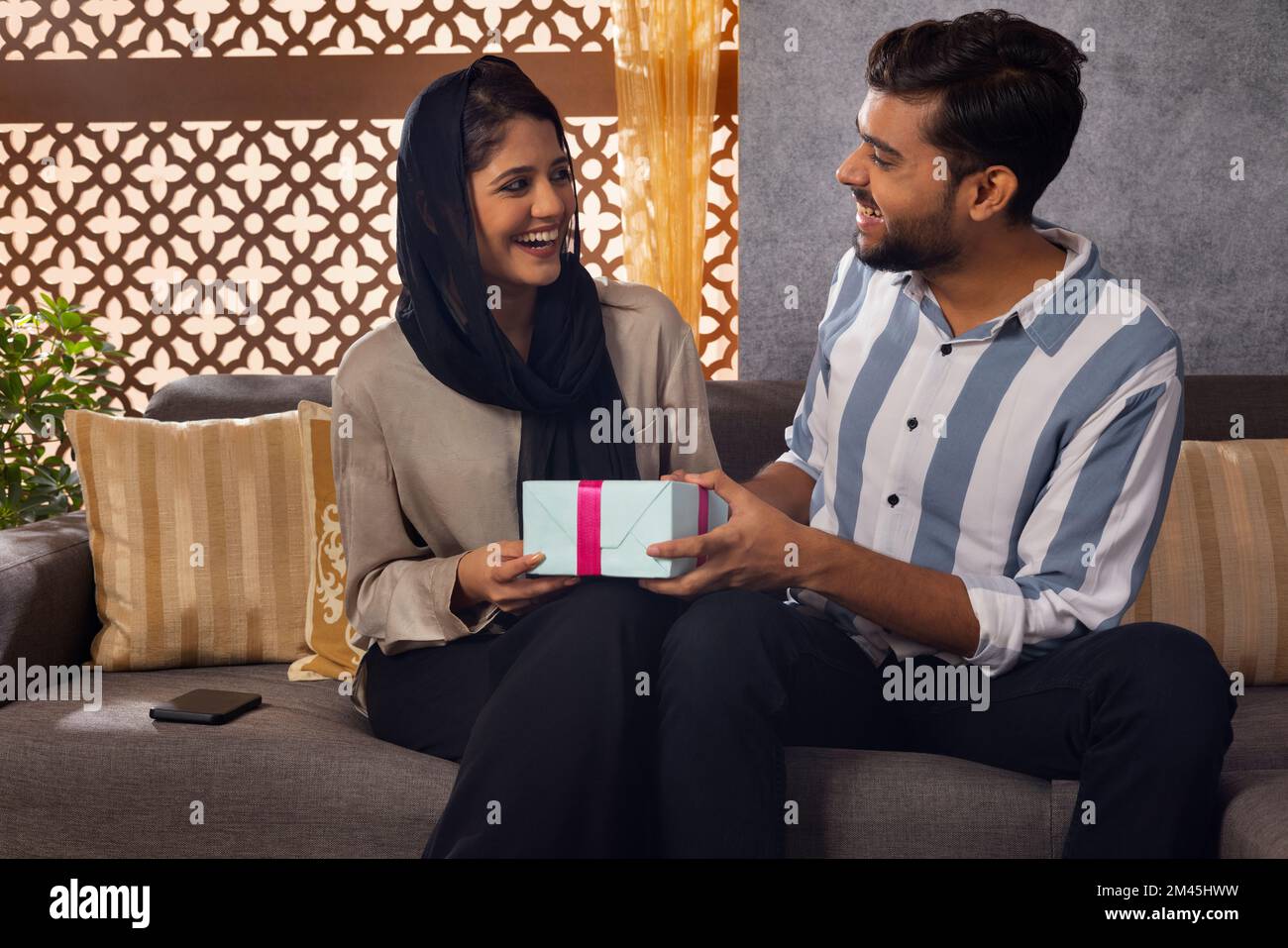 Muslim man giving gift to his happy wife sitting on sofa at home Stock ...