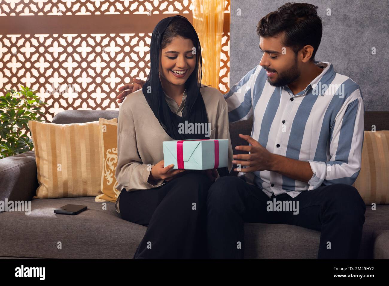 Muslim man giving gift to his happy wife sitting on sofa at home Stock ...