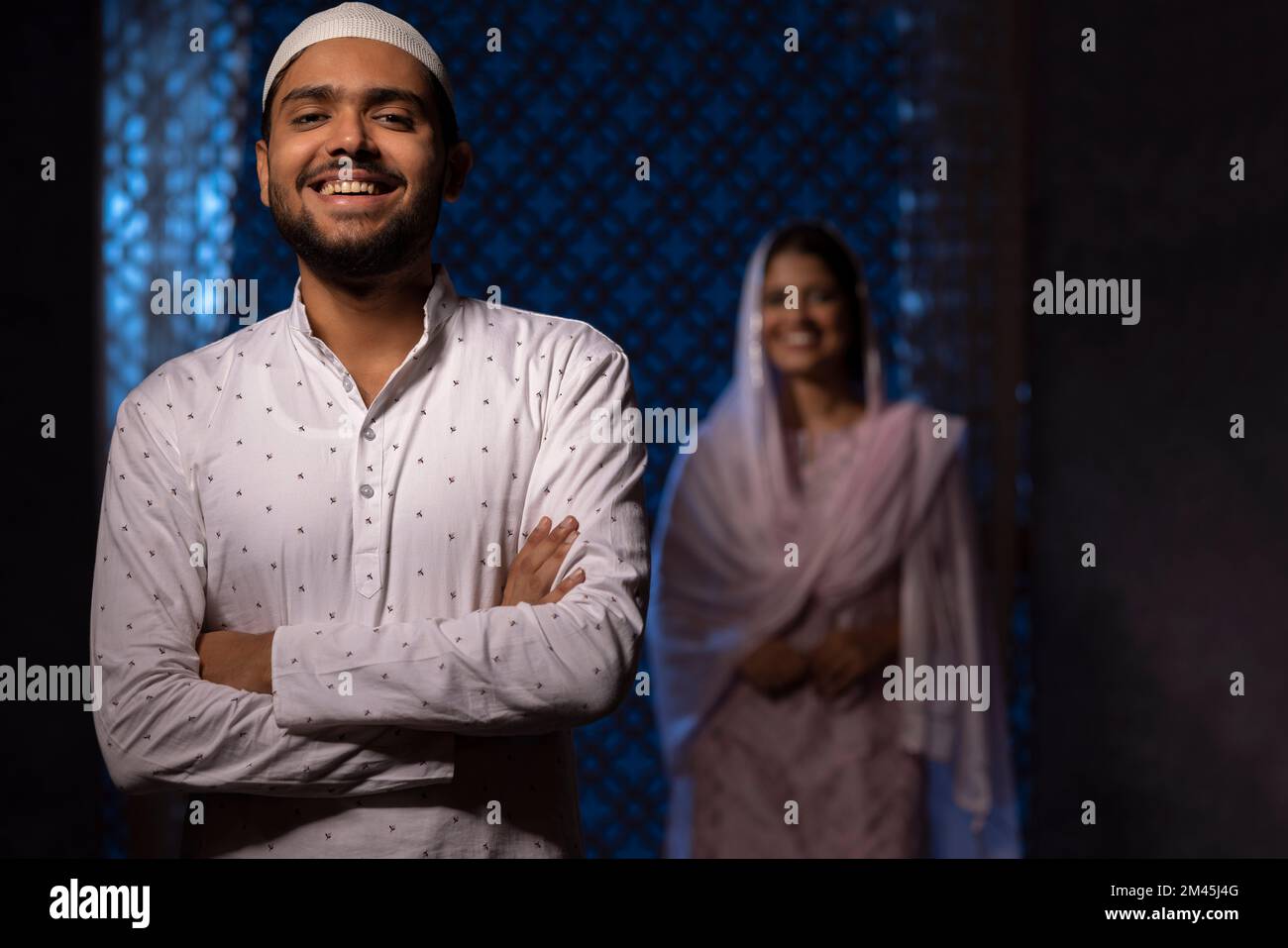 Muslim man looking at camera with folded hands while his wife standing ...