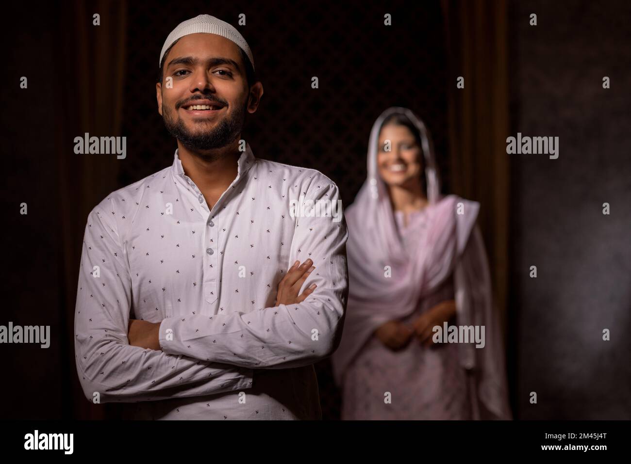 Muslim man looking at camera with folded hands while his wife standing ...
